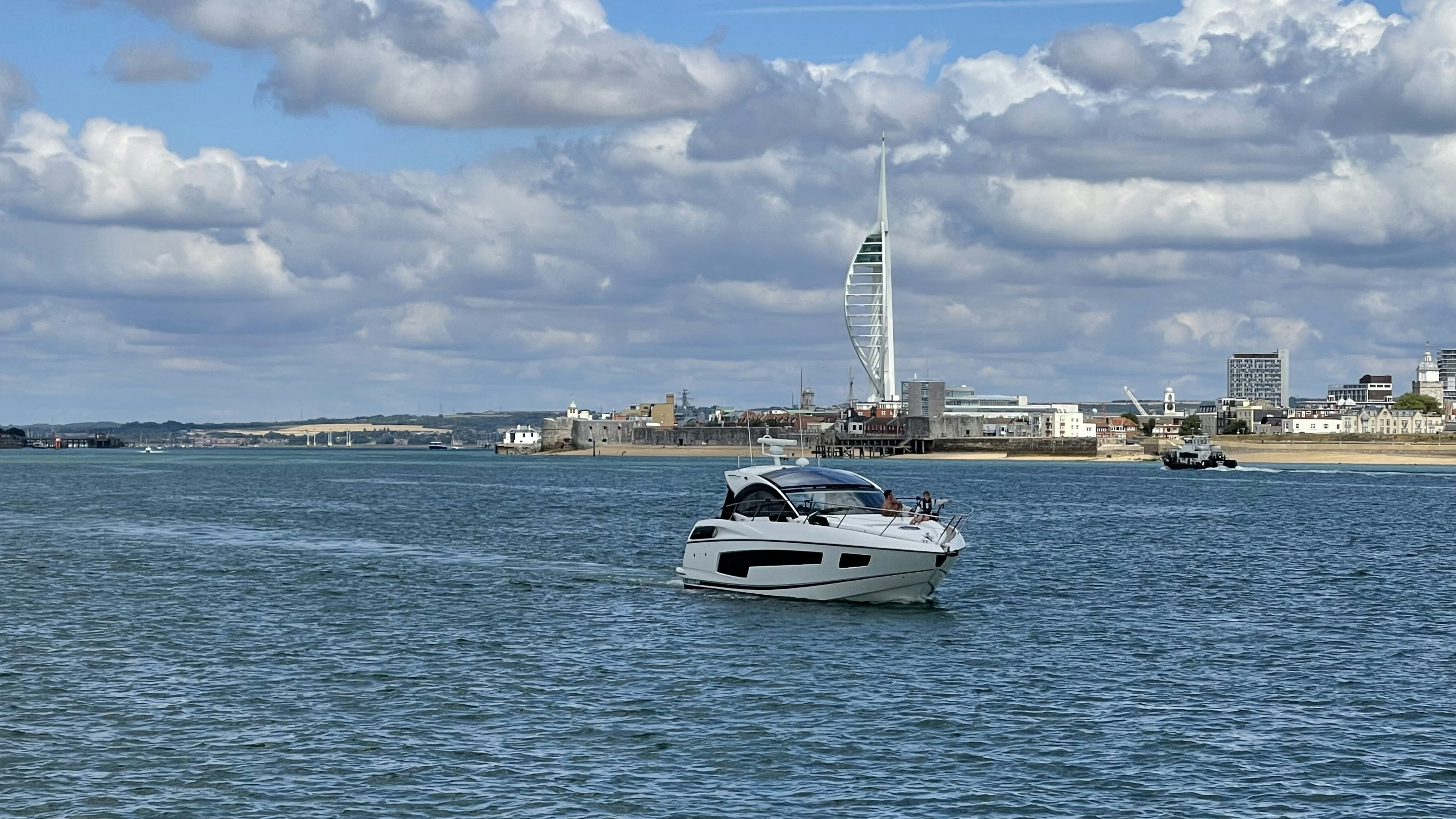 Luxury motorboat navigating calm waters with a coastal city skyline in the background, showcasing modern architecture and a vibrant atmosphere.