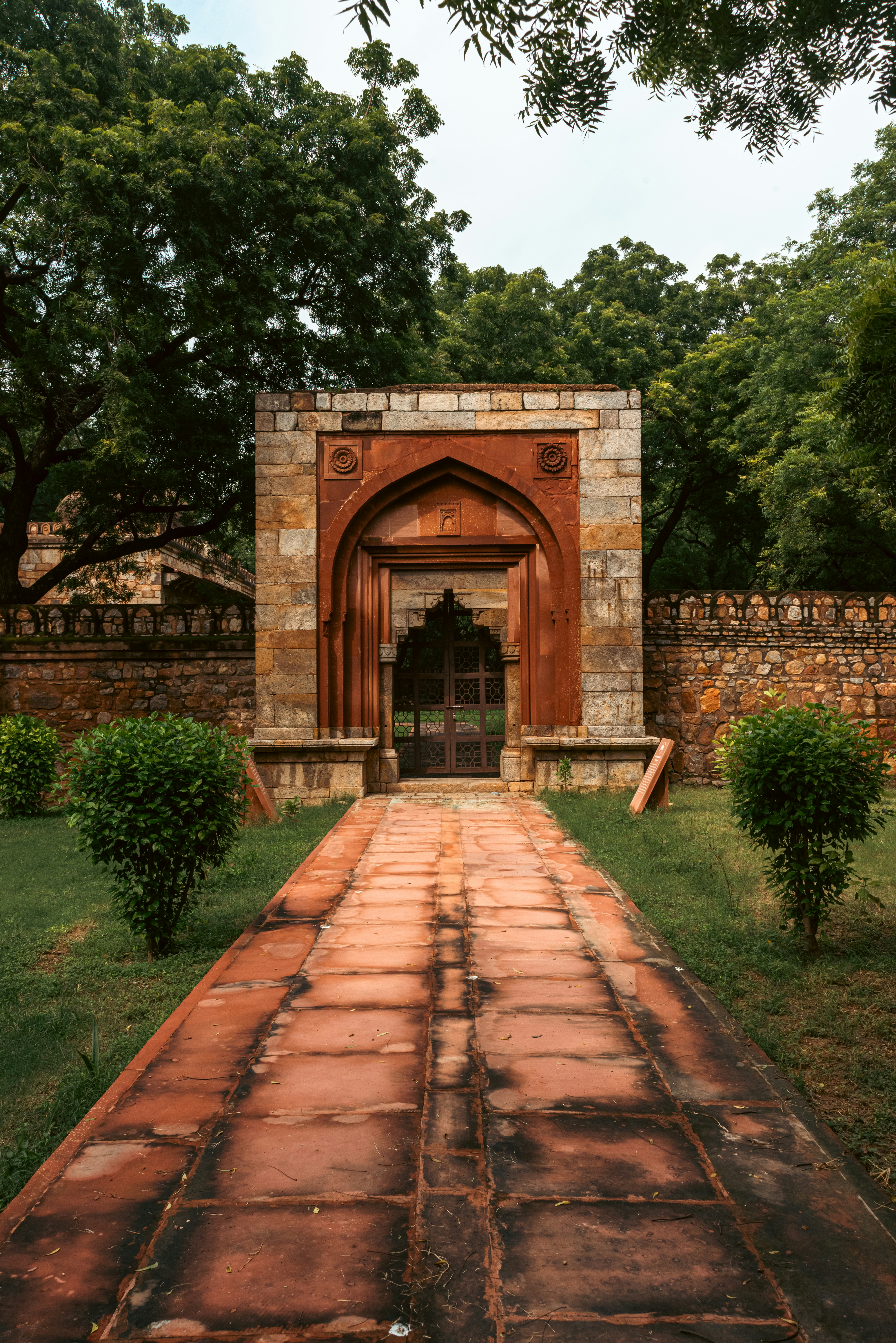 Intricately designed archway framed by lush greenery, leading to a historic site. The pathway invites exploration.