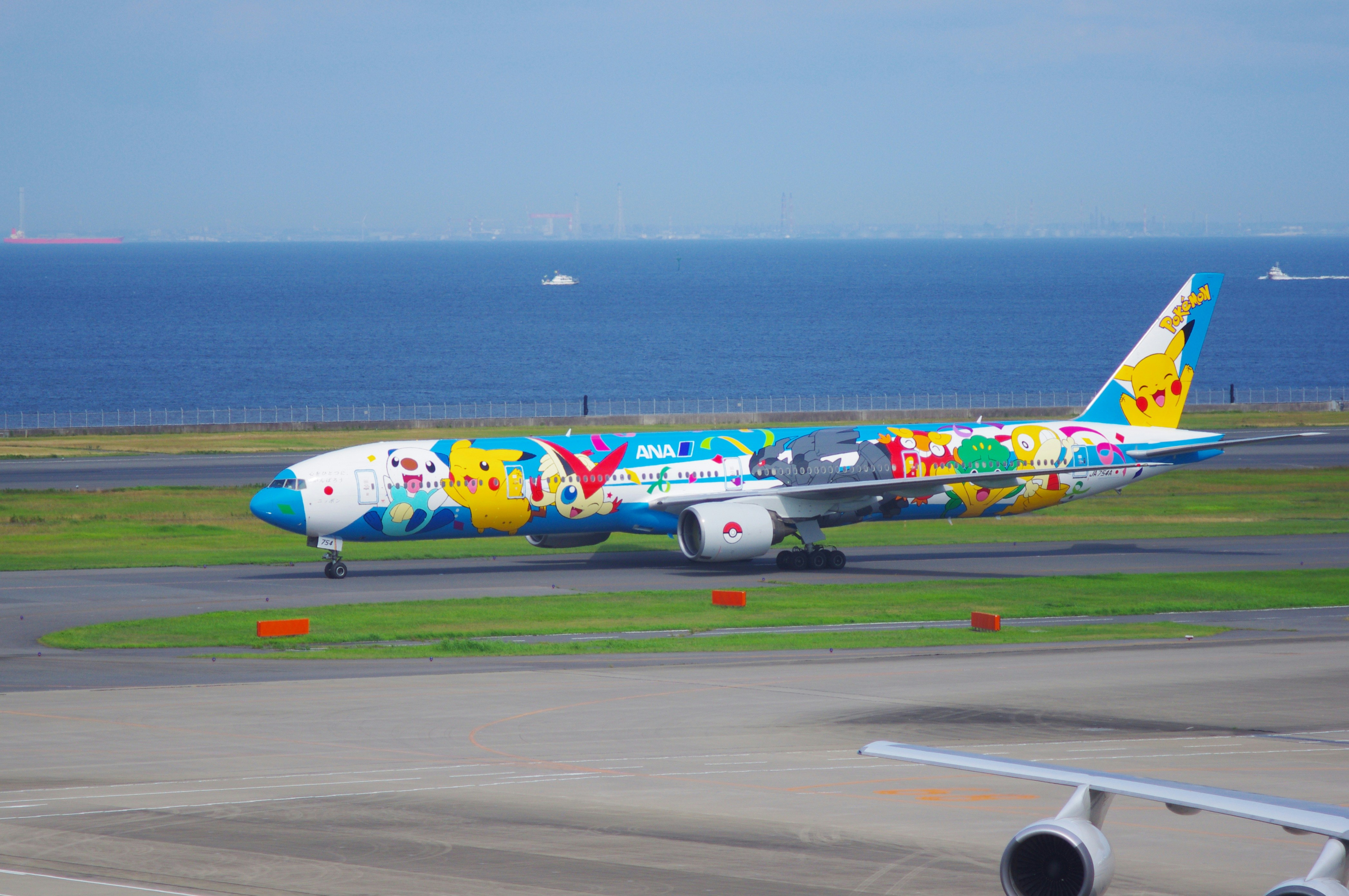 ANA airplane adorned with vibrant, playful designs taxiing on the runway beside a serene ocean backdrop.