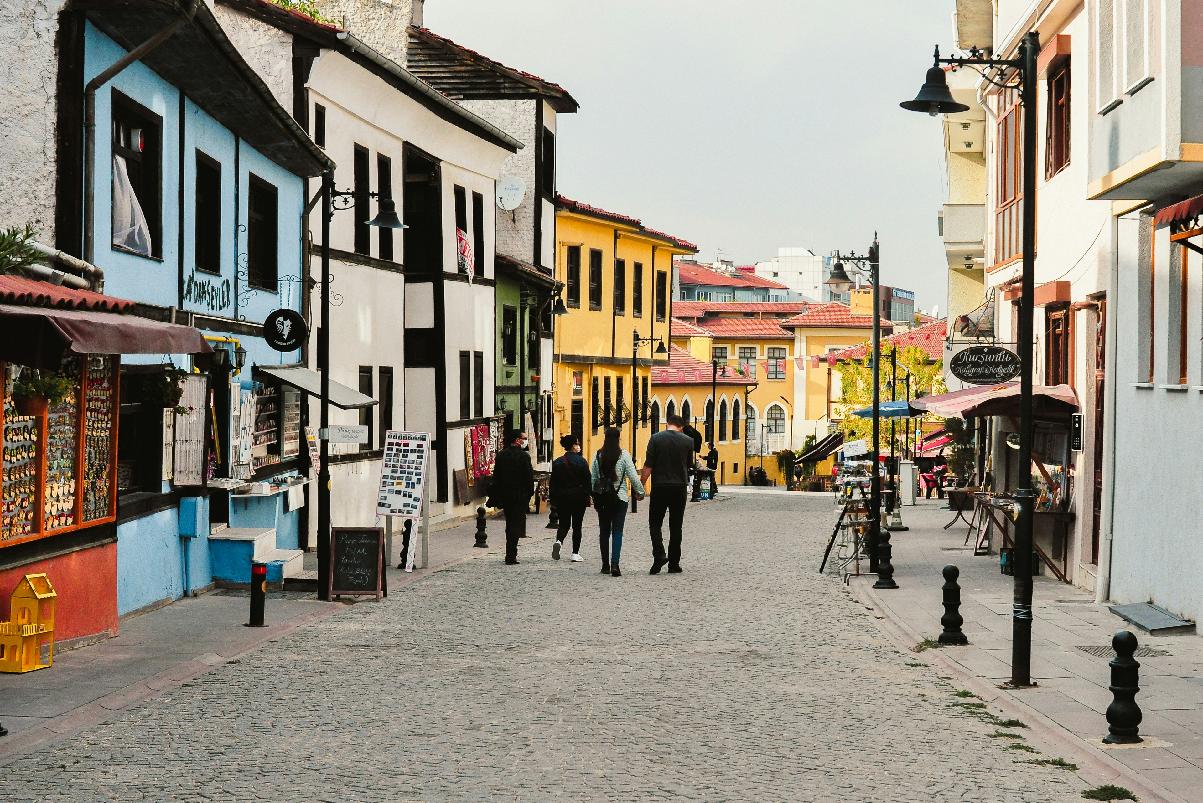 Walking through the colorful streets of Odunpazarı feels like stepping into a living museum — every wooden house, narrow alley, and handmade detail tells a story of Eskişehir’s warm soul and timeless charm. | People walking down a colorful, historic european street.