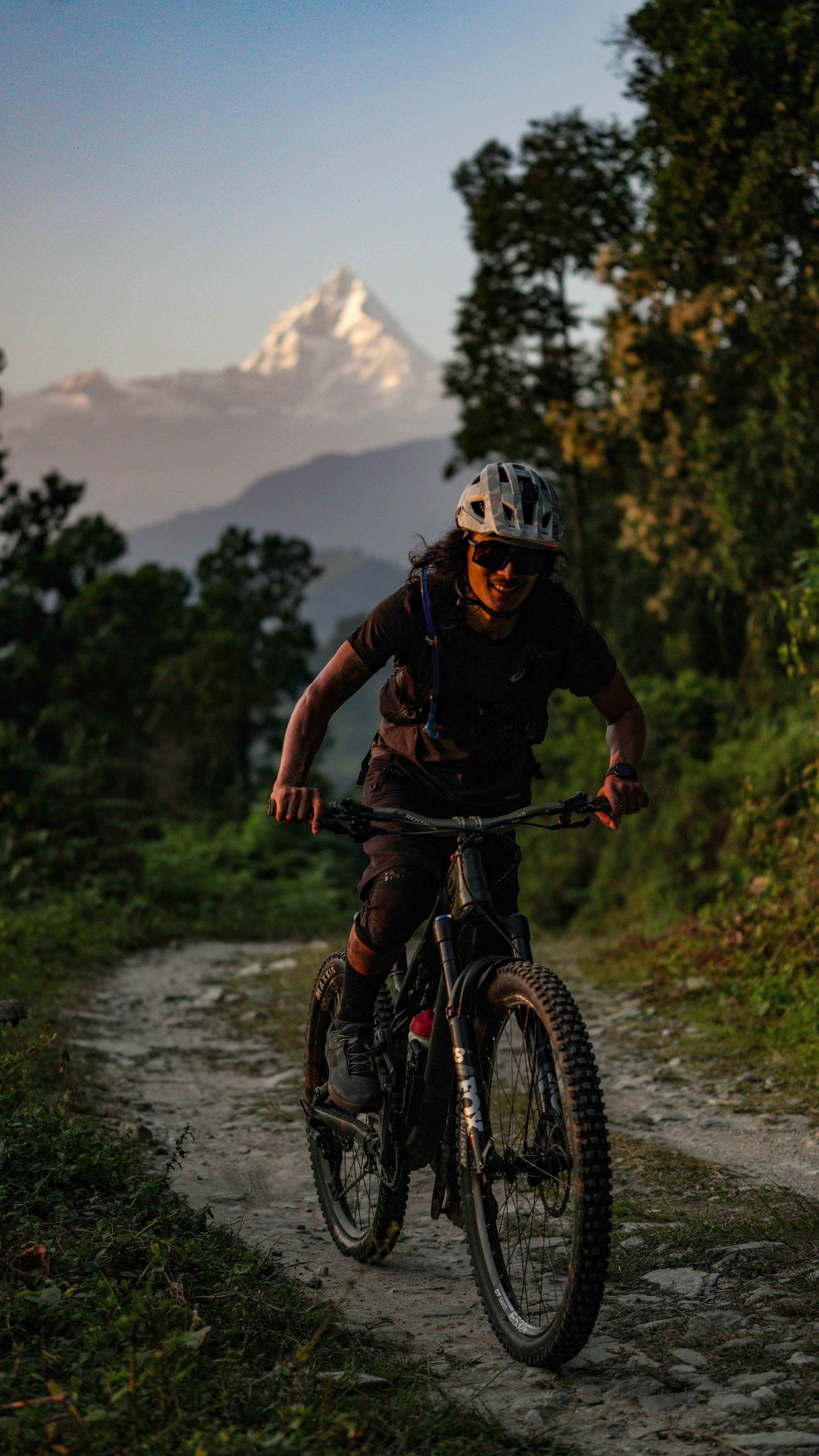 Golden Hour Ascent: Mountain Biker Navigates a Rugged Trail Toward a Snow-Capped Summit