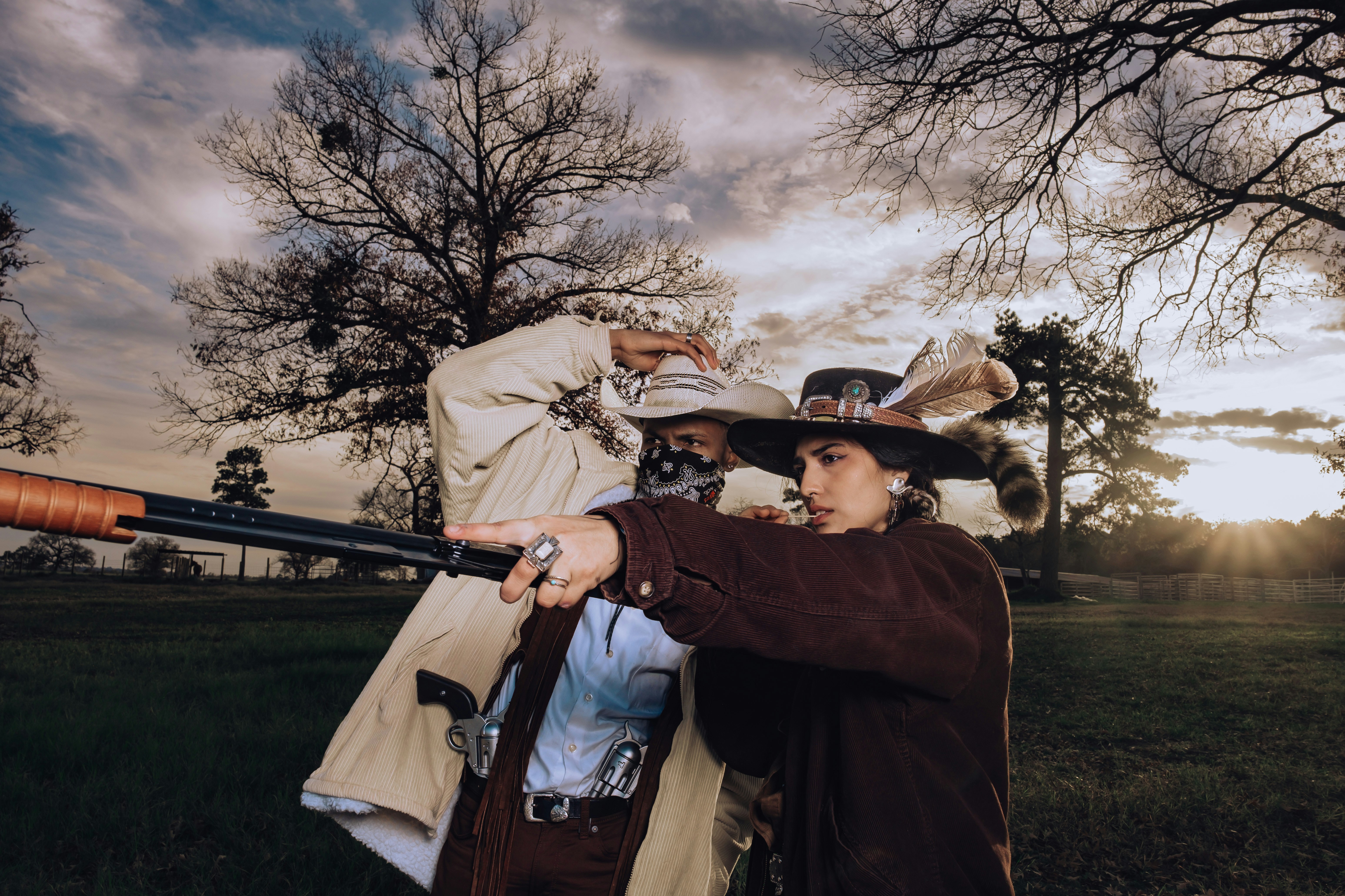 Two people in cowboy hats with a rifle at sunset.