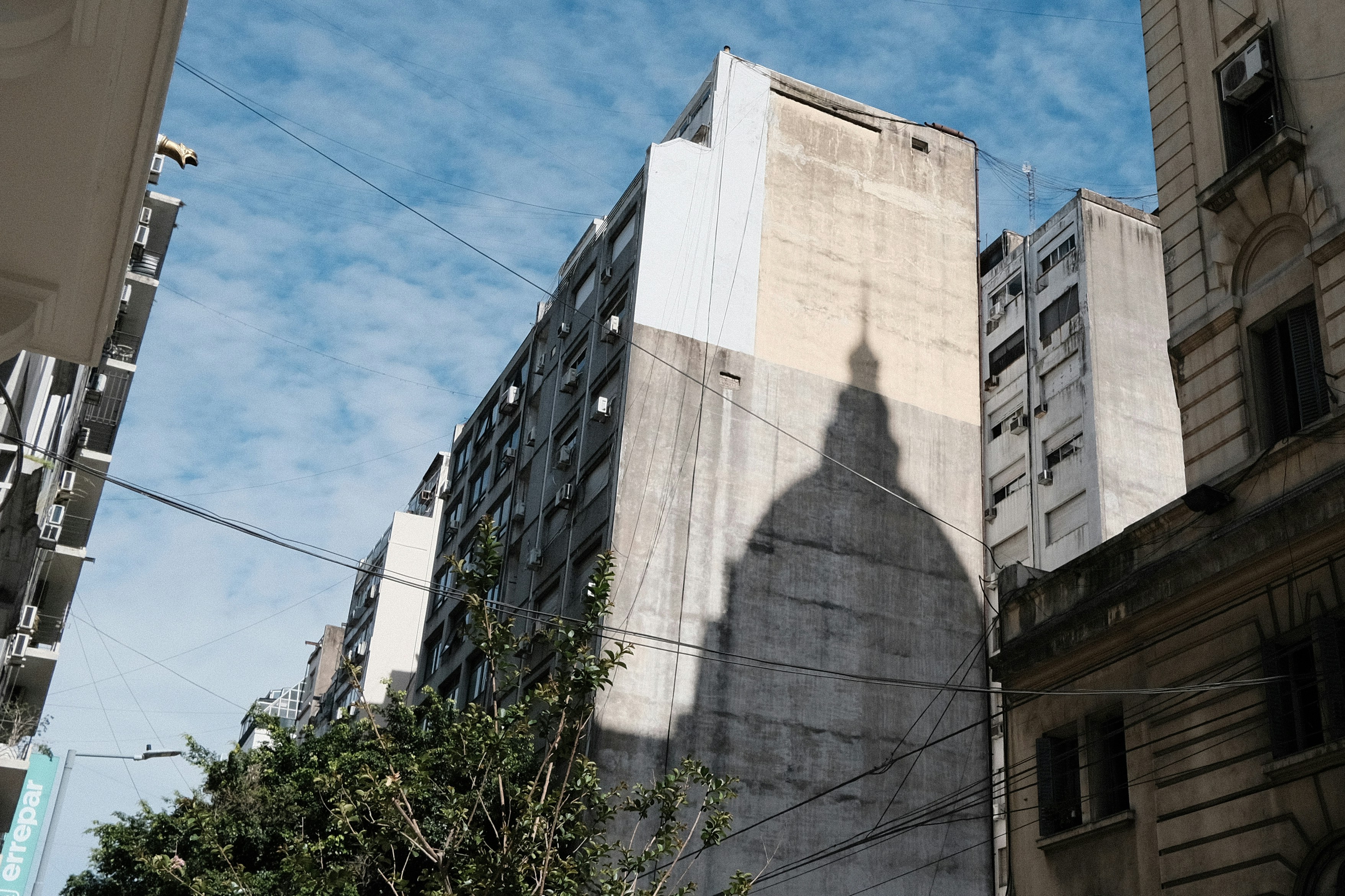 A tall building casts a prominent shadow resembling a dome onto a textured wall in a bustling urban setting.