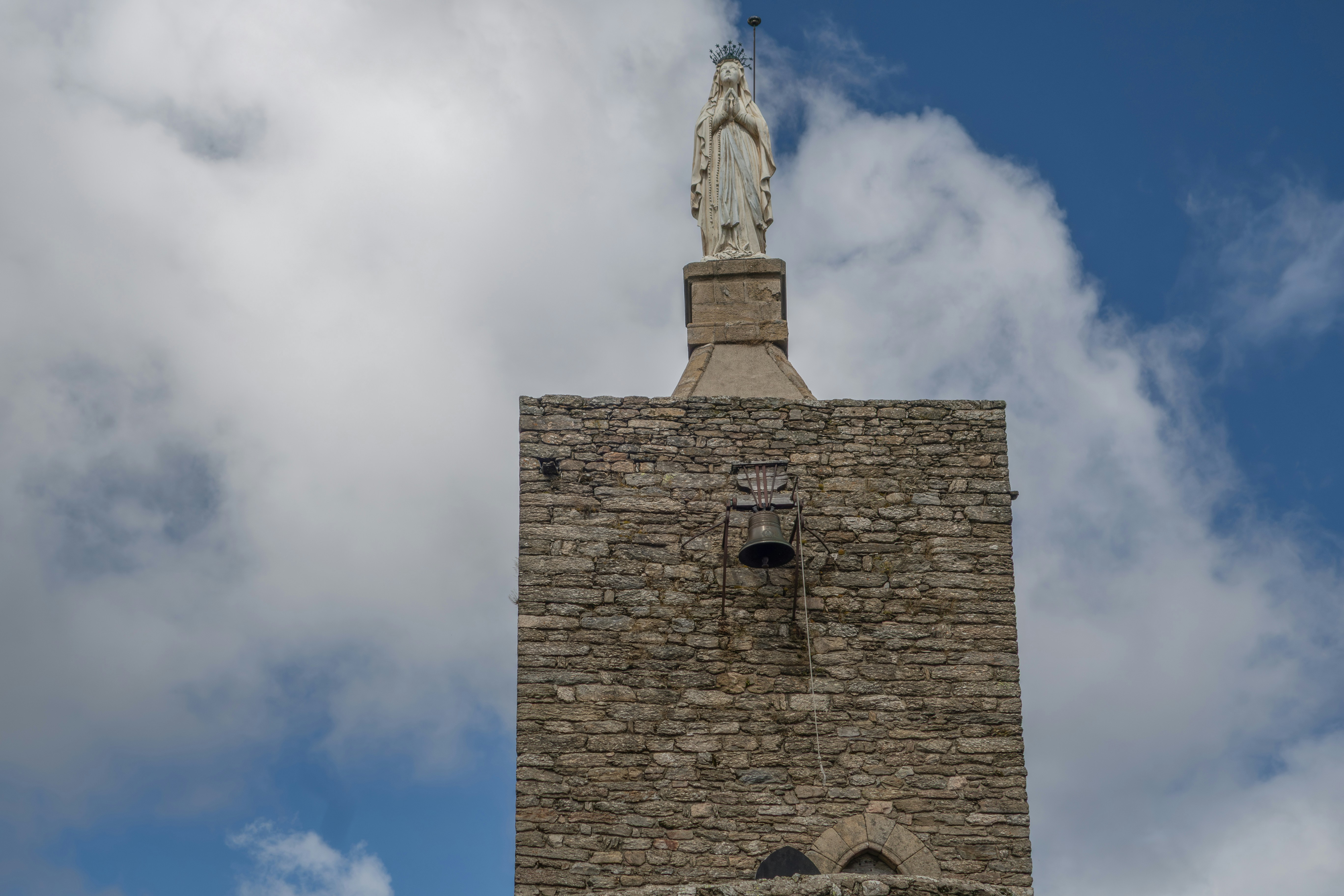 A towering stone structure crowned with a statue, set against a backdrop of dynamic clouds. The scene conveys a sense of history and reverence.