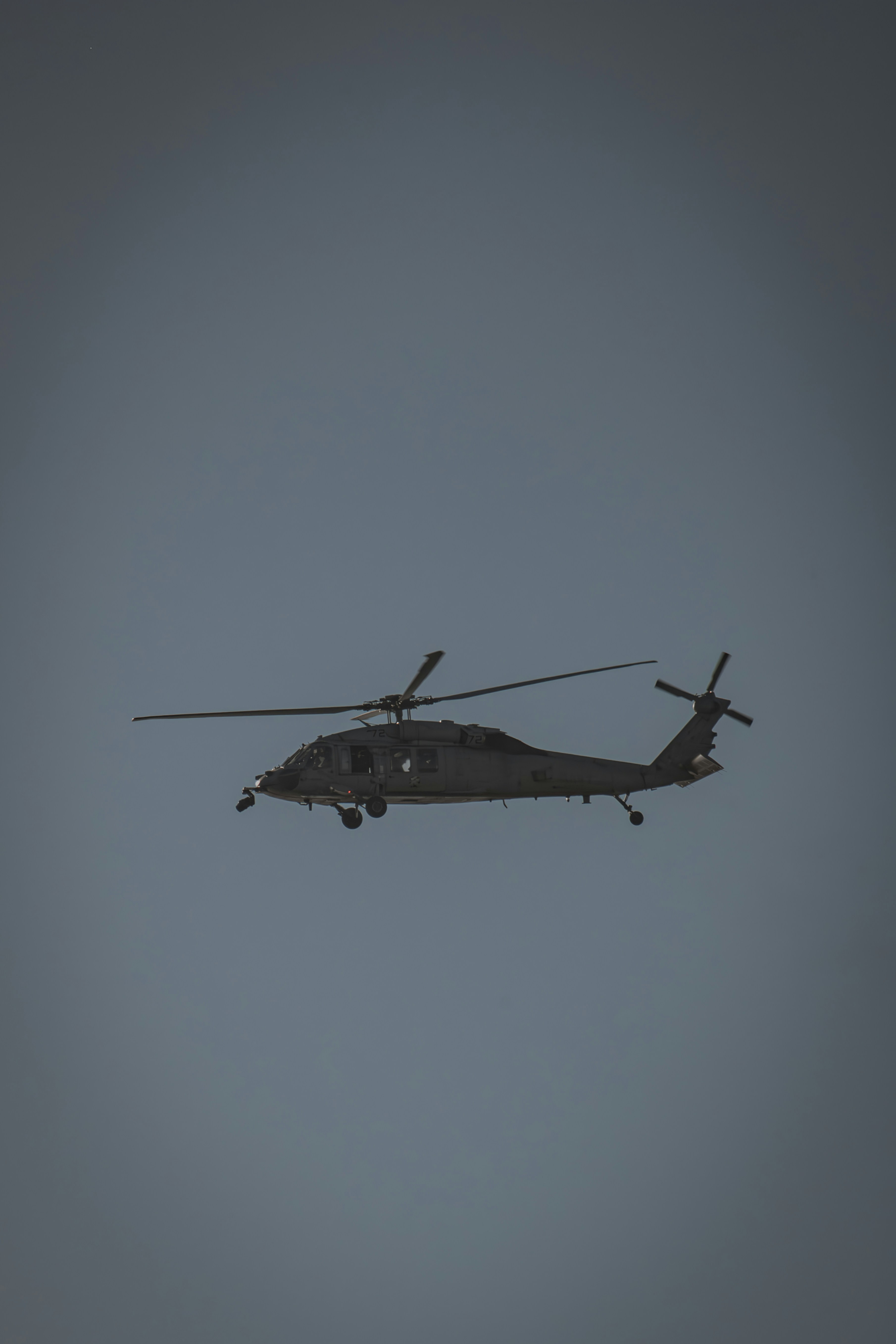 Midair silhouette in a gray haze: a helicopter glides across a diffused horizon