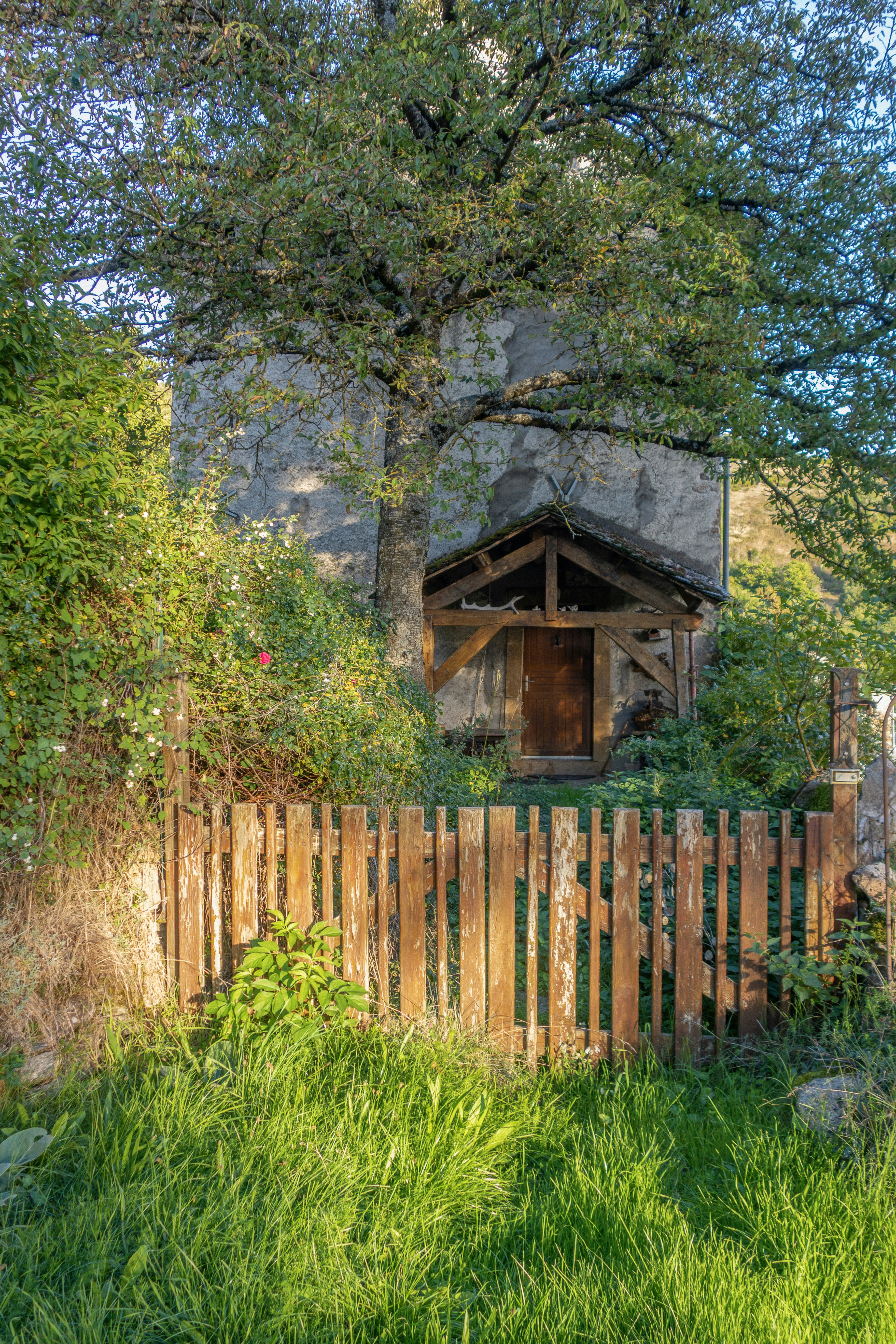 Sur ce chemin, l’homme ne conquiert rien. Il écoute. Il marche entre les pierres et les nuages, là où Stevenson jadis chercha le silence et la vérité. Chaque pas est une mémoire, chaque paysage une page ouverte. Ce n’est pas la France qu’on traverse, mais un monde en miniature — fait de lumière, de solitude, et d rencontres. | Rustic wooden fence in front of old stone building