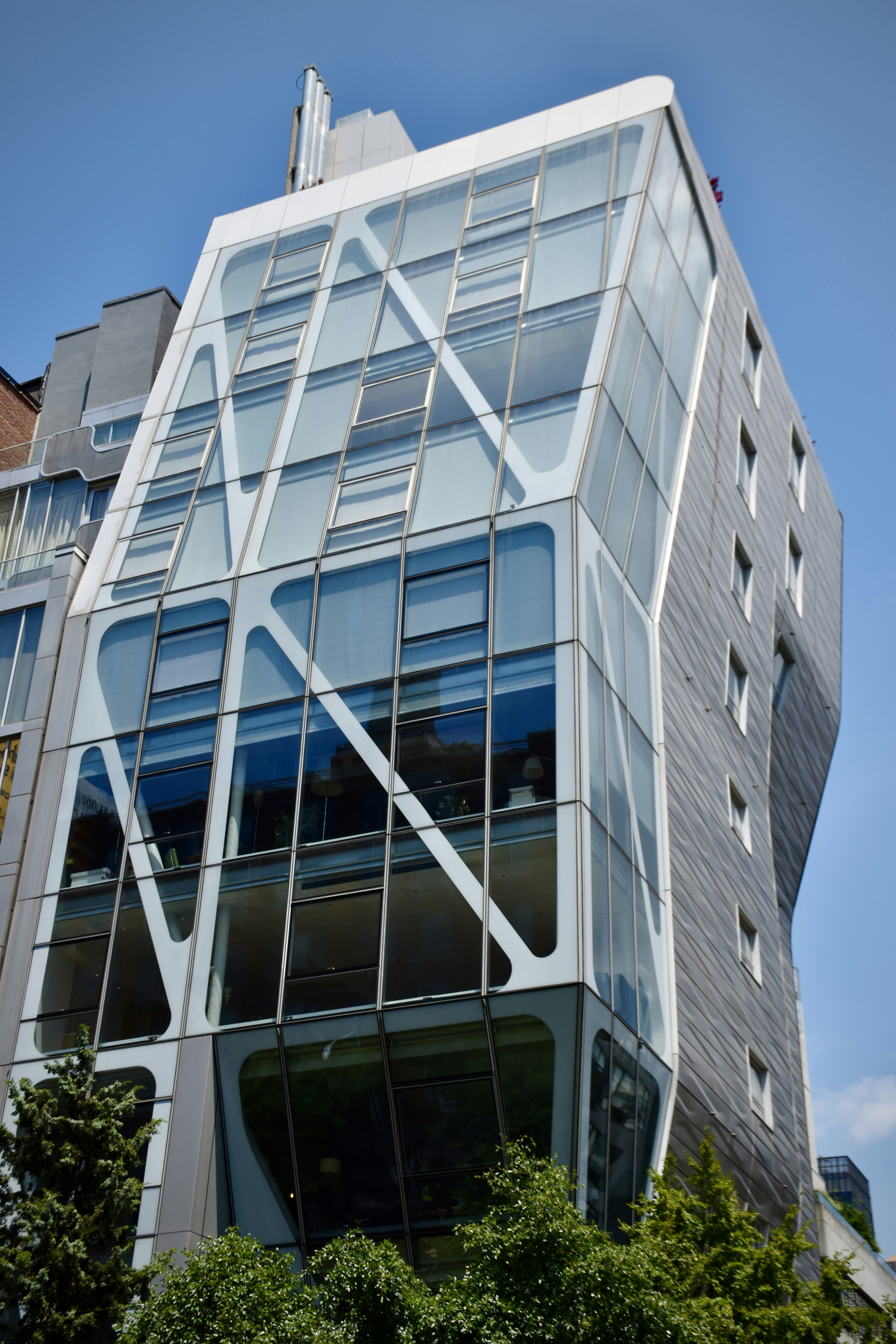 Innovative building design featuring a glass and wood exterior with distinctive geometric patterns. Surrounded by greenery, it exemplifies contemporary architecture.