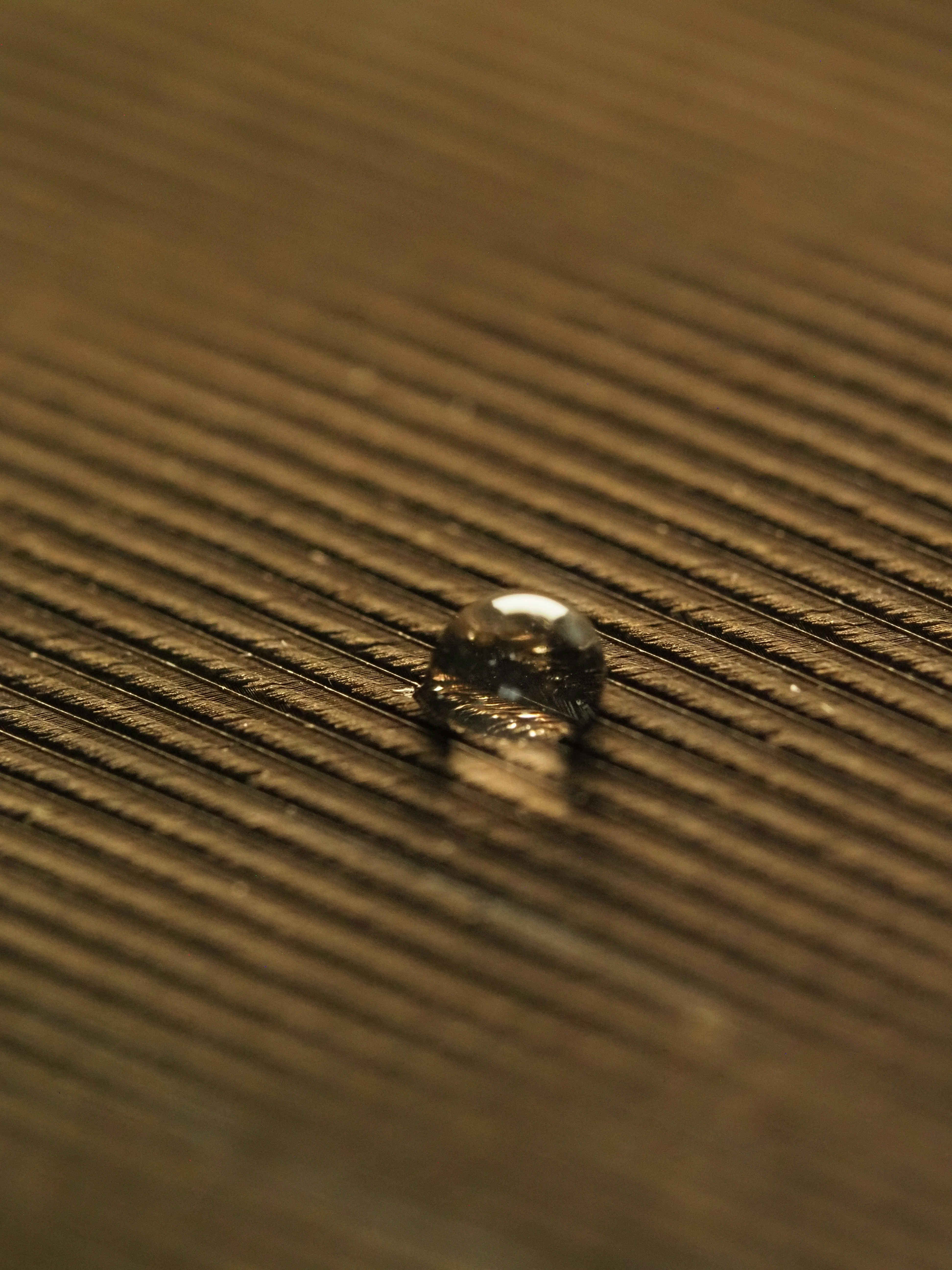 A single water droplet resting on a textured surface, showcasing intricate reflections and patterns. The image highlights the interaction between water and the material beneath it.