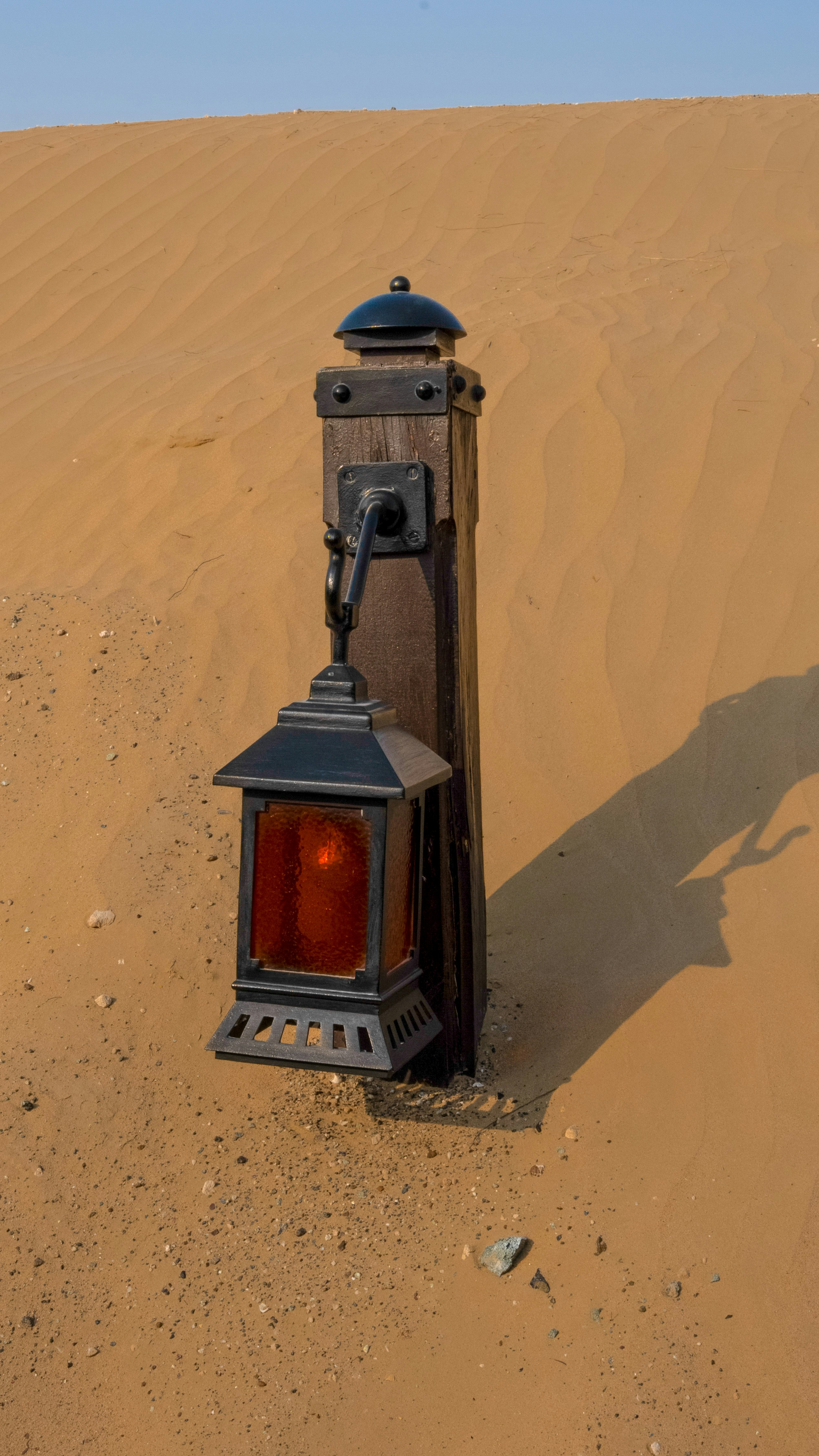 Light that no one else sees. This red lantern in an infinite desert is a perfect metaphor for humanity: we create lights in darkness, then abandon them. | Lantern hanging on a wooden post in the desert.