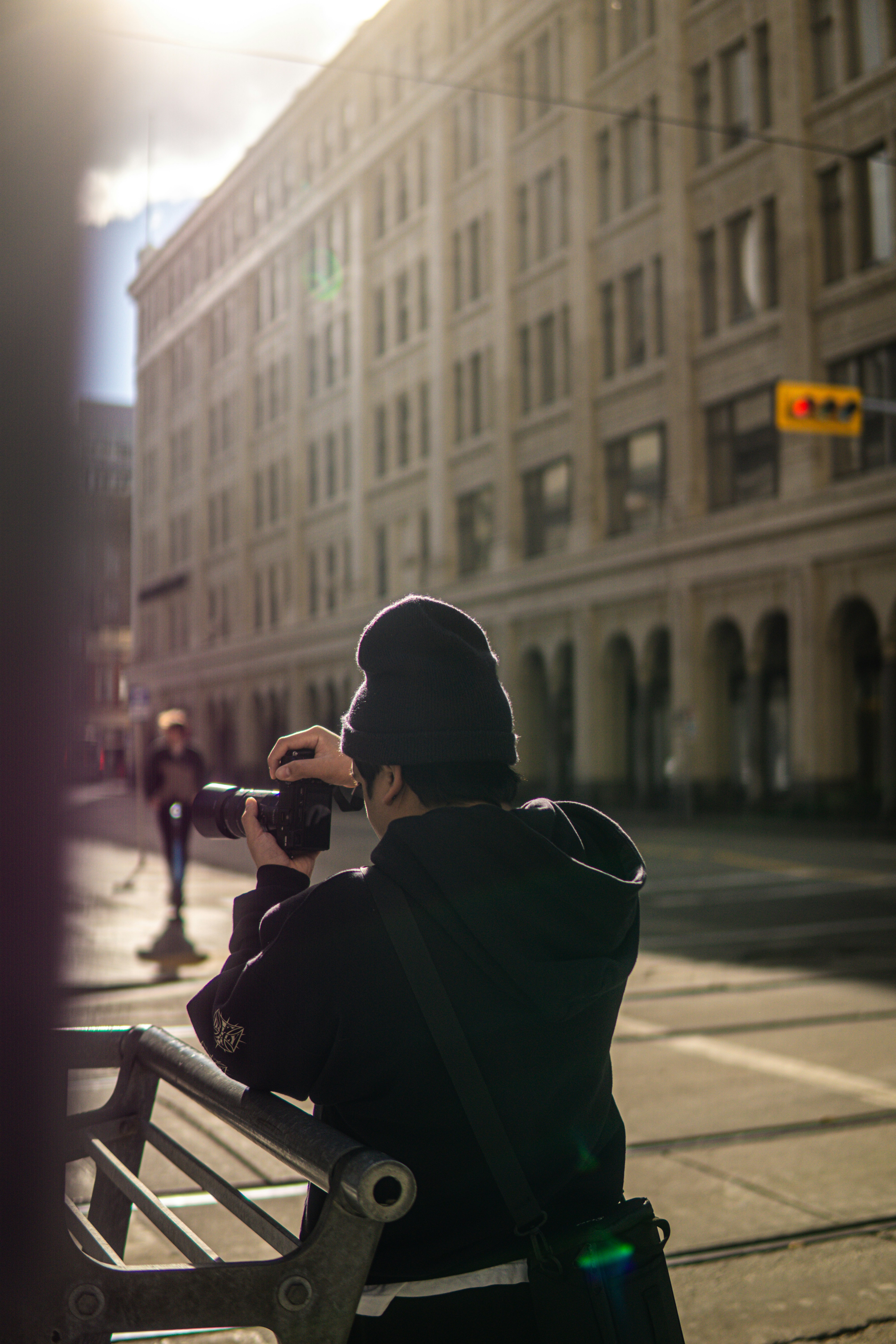 A photographer poised to capture the essence of a bustling city street, framed by historic architecture and soft sunlight.