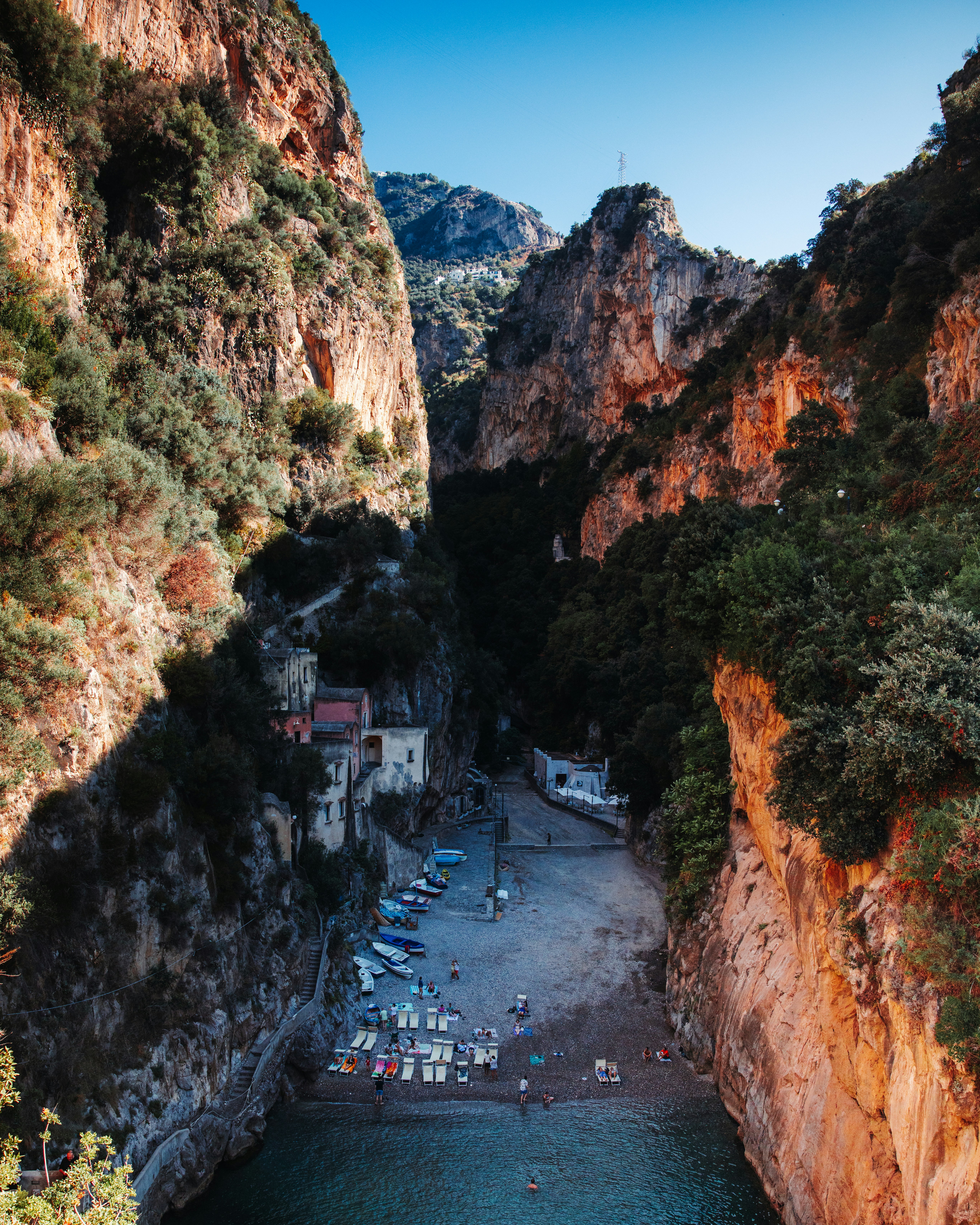 Secluded beach nestled between towering cliffs, featuring colorful beach umbrellas and boats along the shoreline.