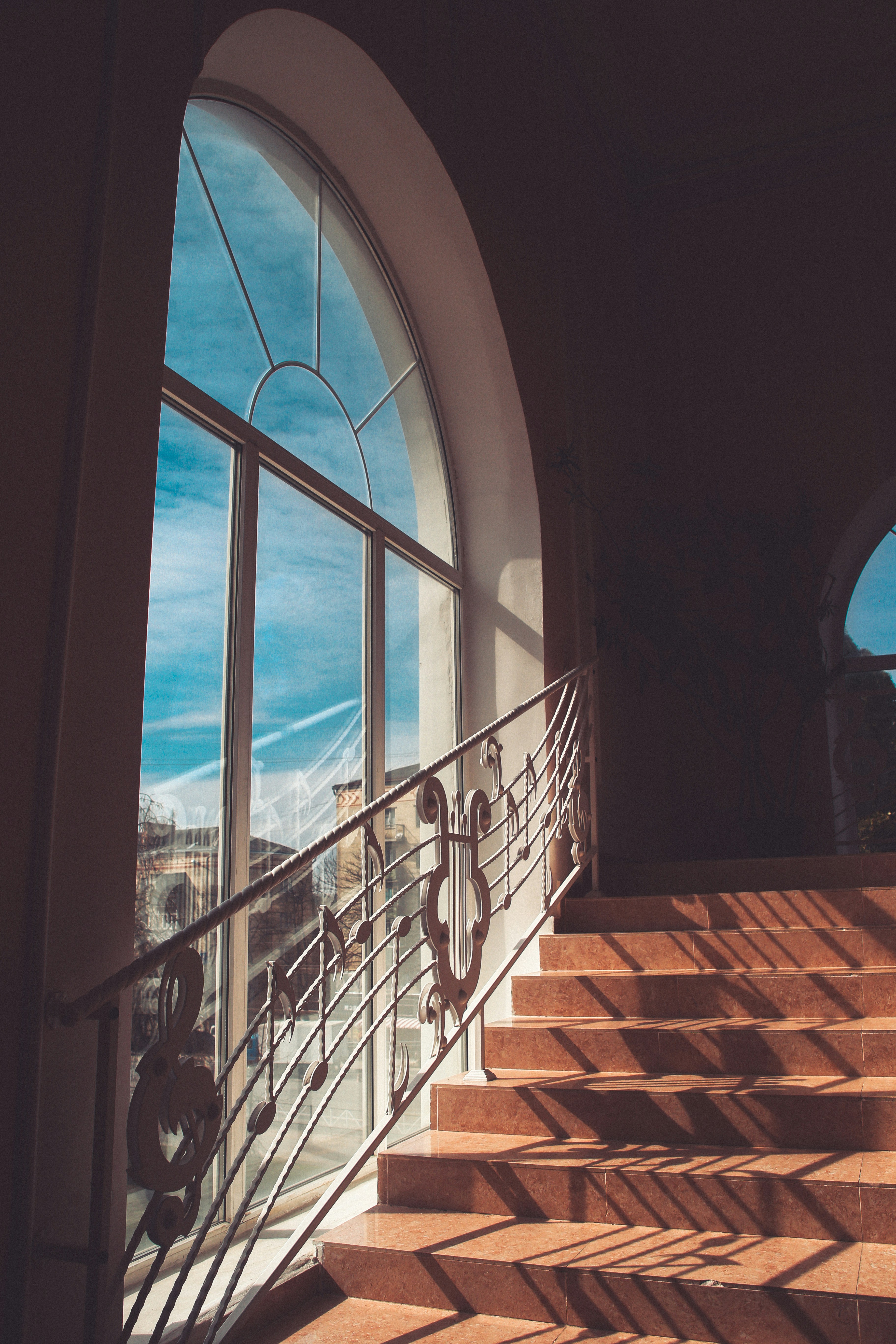 Sunlit staircase with ornate railing and arched window.