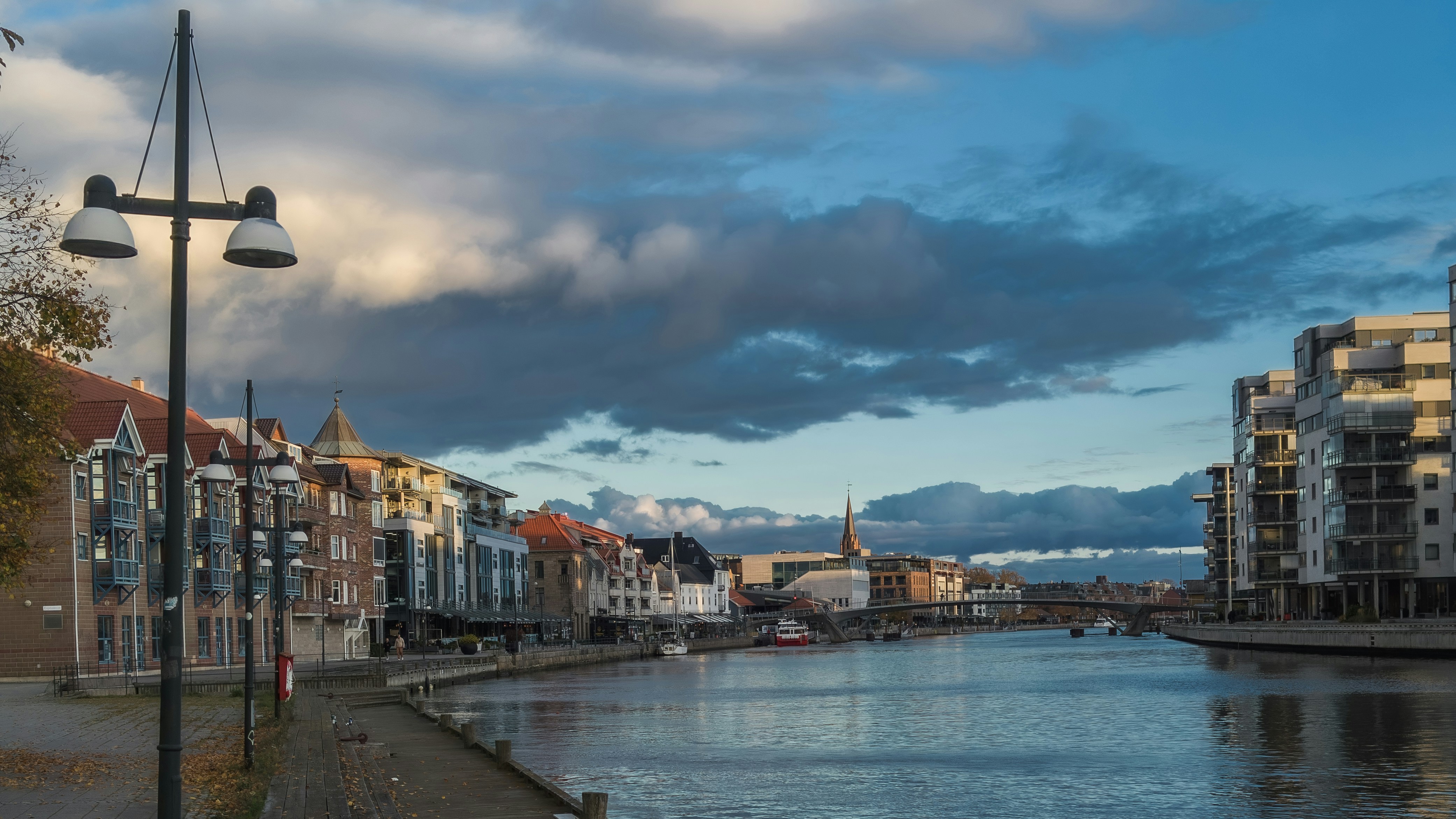 Serene waterfront scene showcasing modern architecture along a canal, with clouds reflecting on the water's surface.