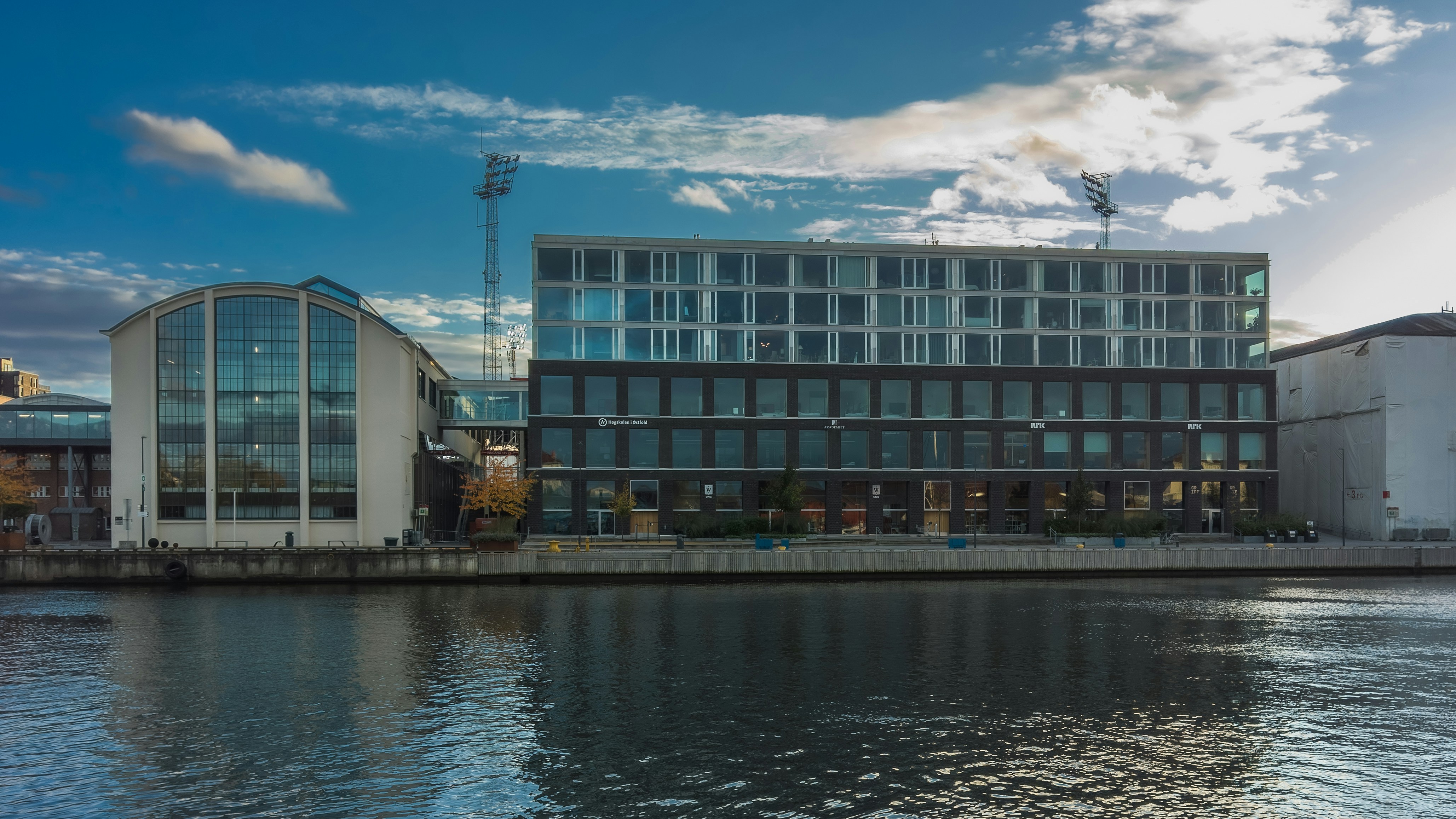 Modern buildings on the waterfront under a cloudy sky.