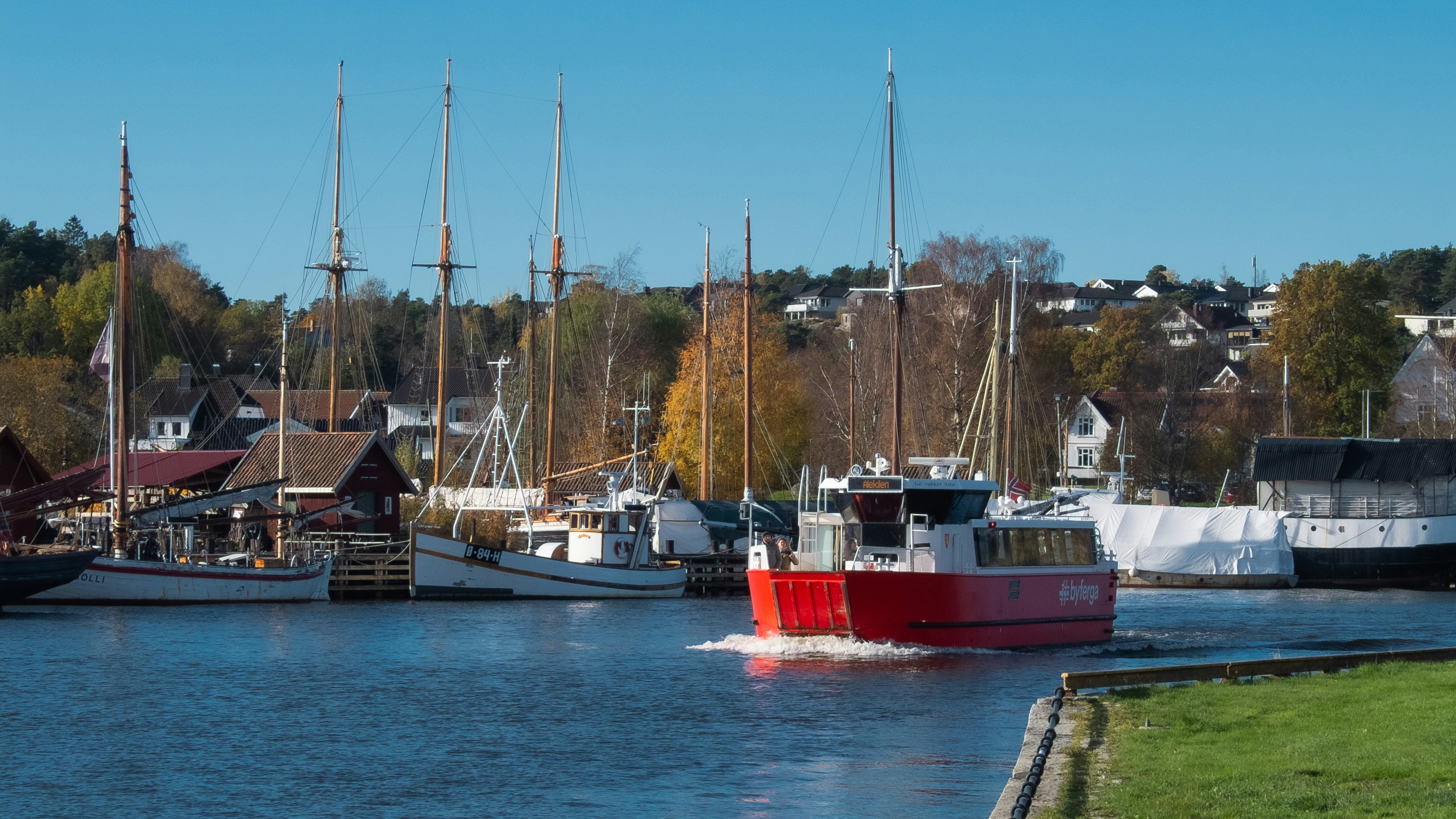 Red ferry boat moving through a harbor with sailboats.