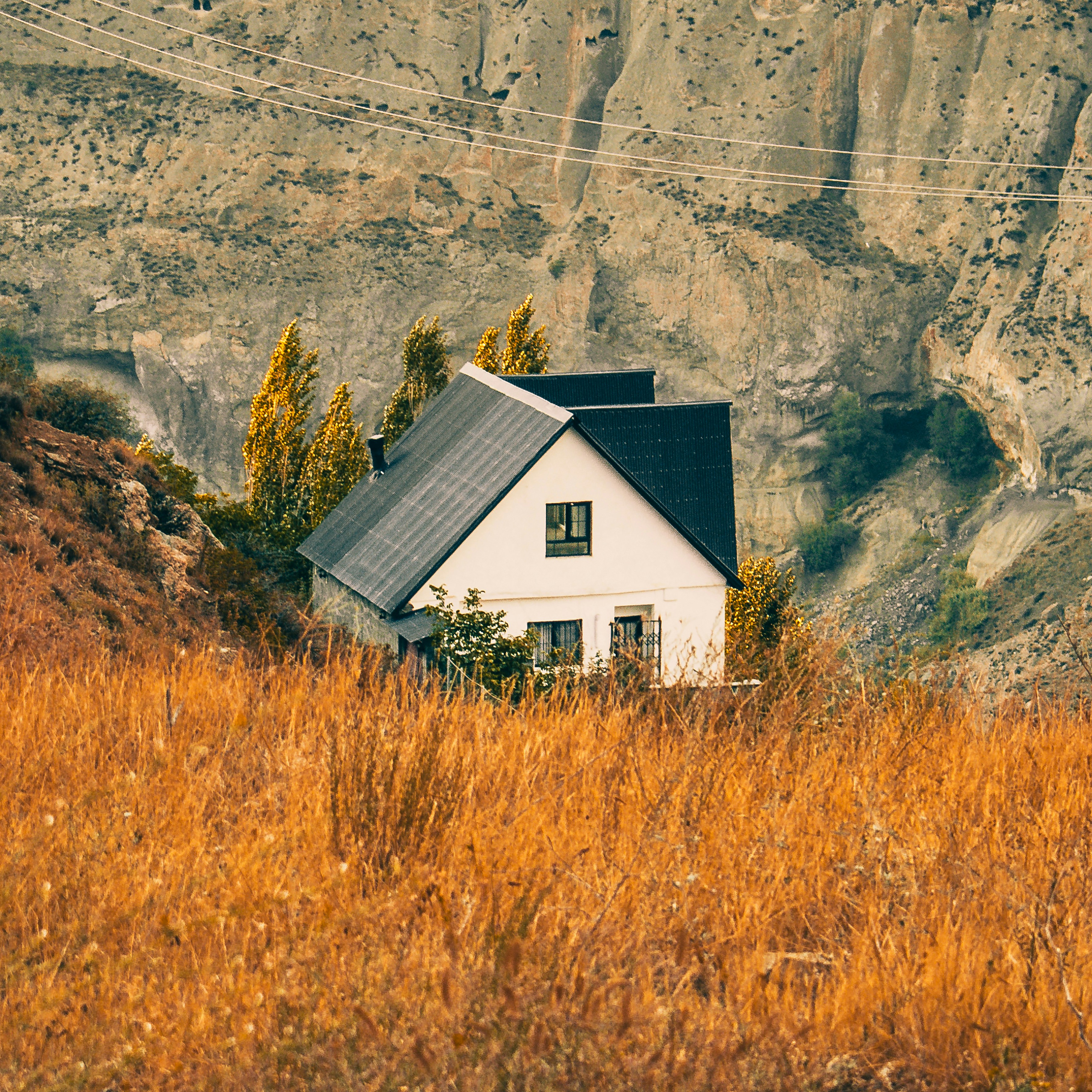 White house nestled in tall dry grass near mountains.