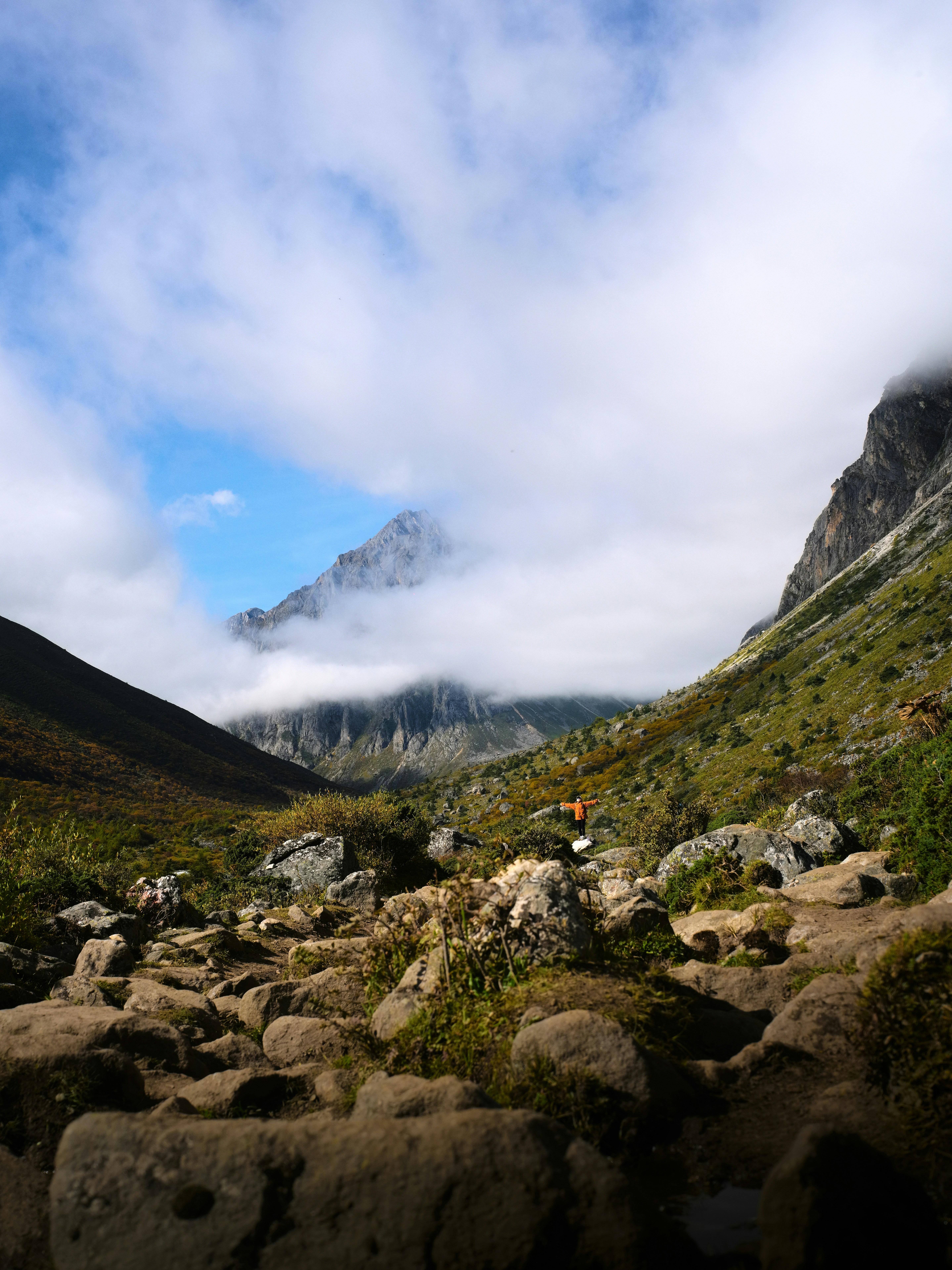 Lush valley shrouded in mist, with rocky terrain leading toward a majestic mountain peak partially obscured by clouds.