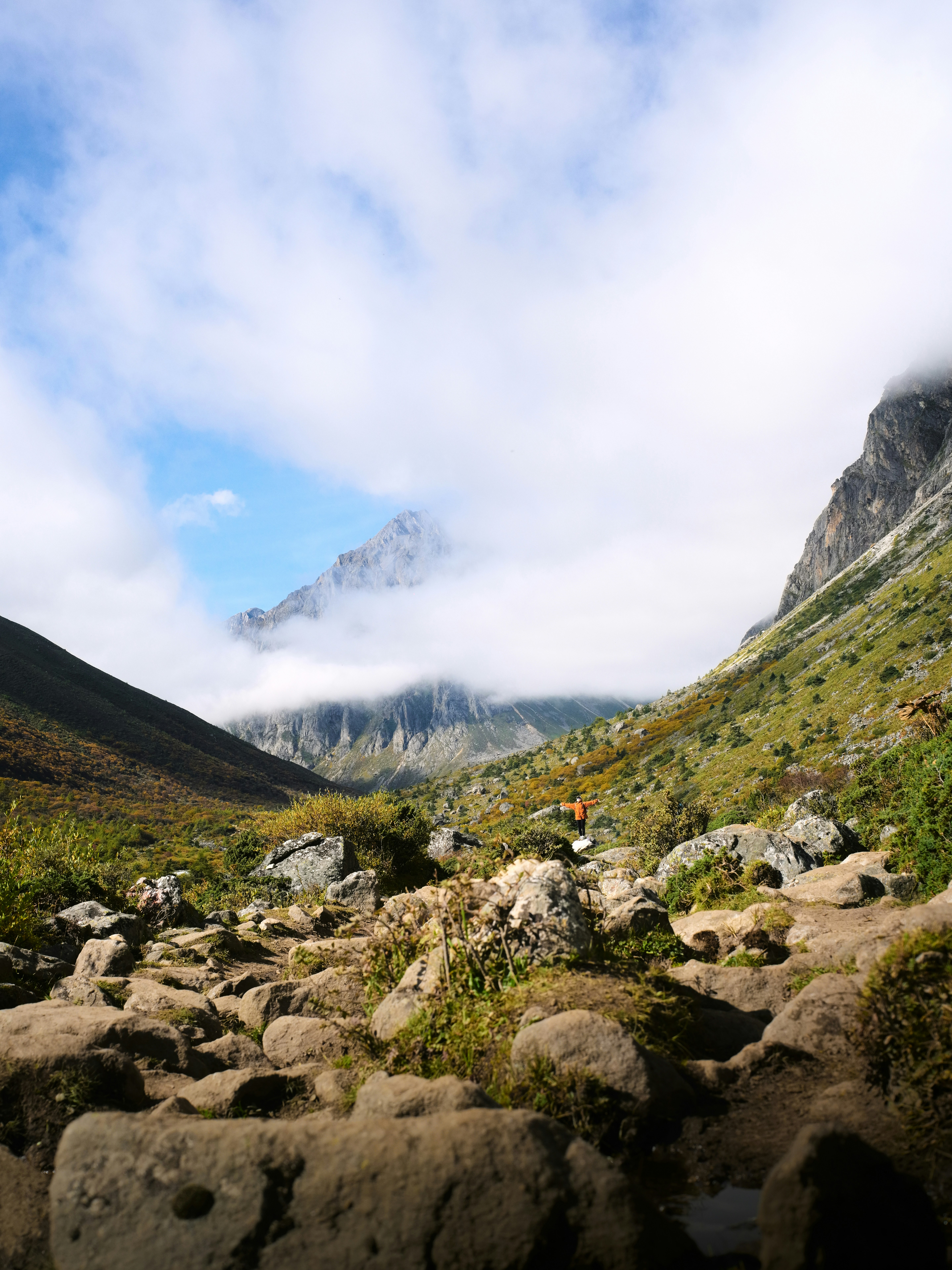 Rocky mountain trail with clouds and green hills