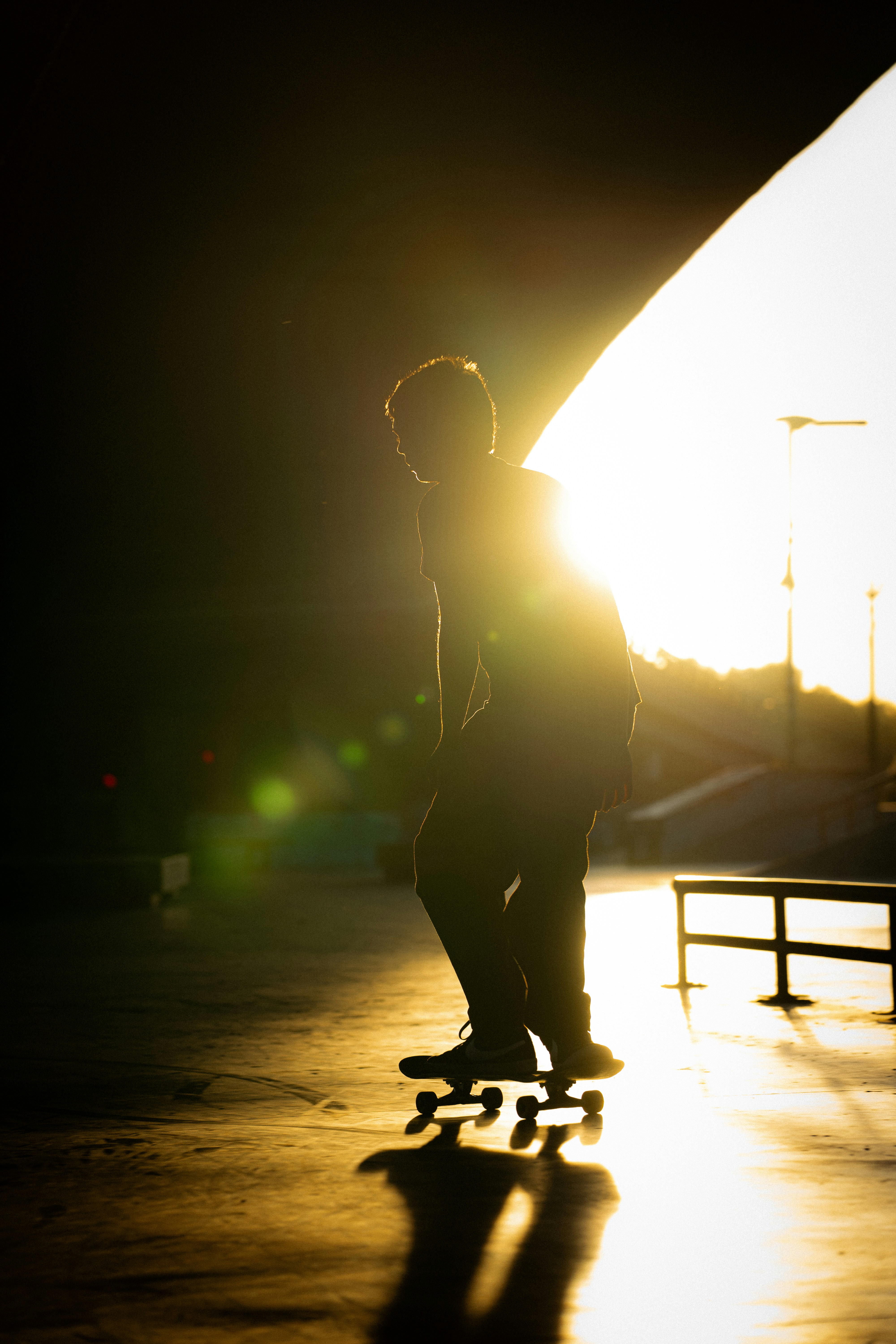 Skateboarder silhouetted against a bright, hazy sunset.