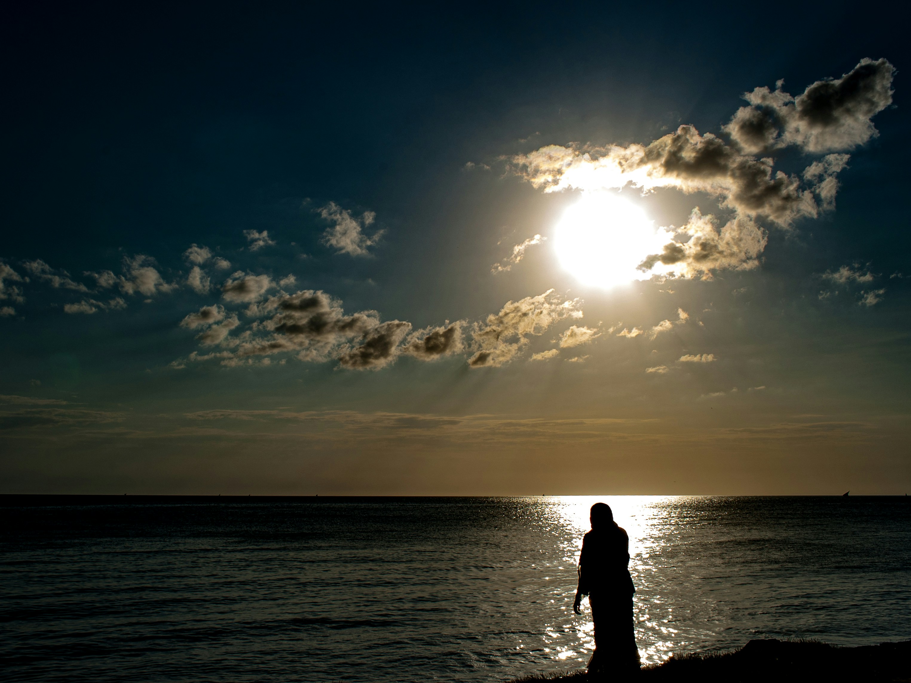 Silhouette of a person standing by the ocean at sunset
