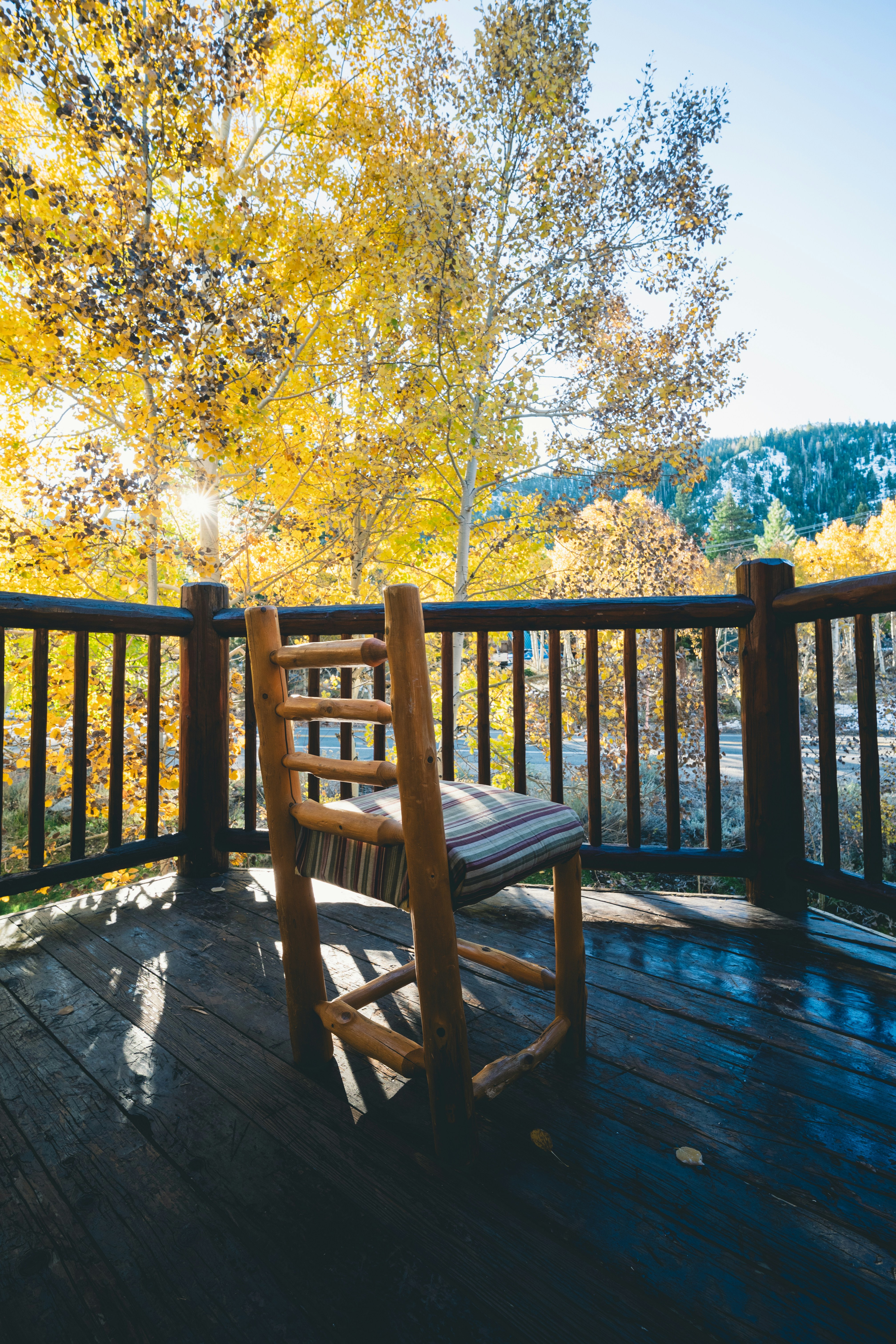 Wooden rocking chair on a deck with autumn trees.