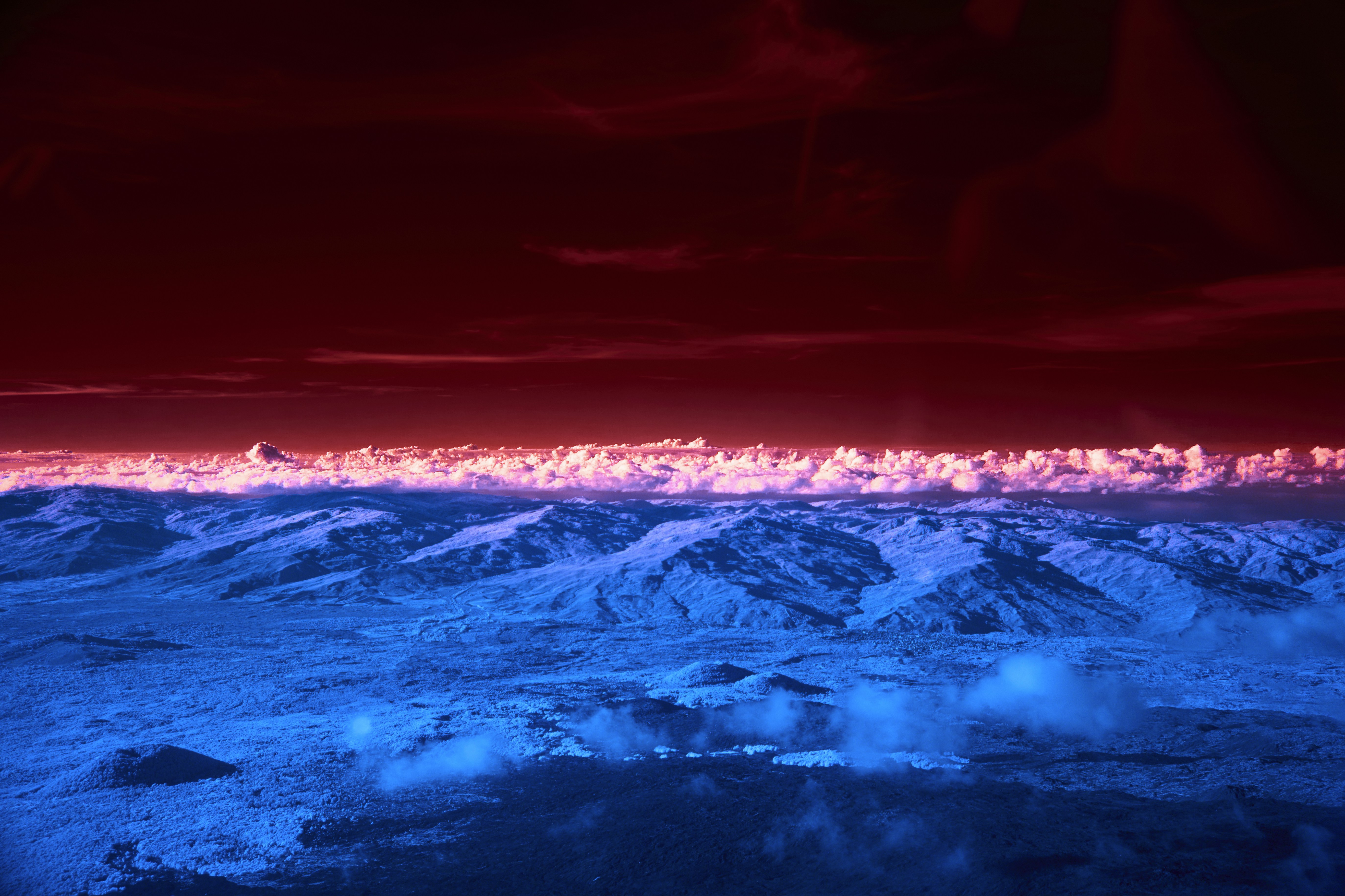 Vividly colored landscape showcasing a dramatic interplay of red and blue hues over snow-capped mountains and clouds.