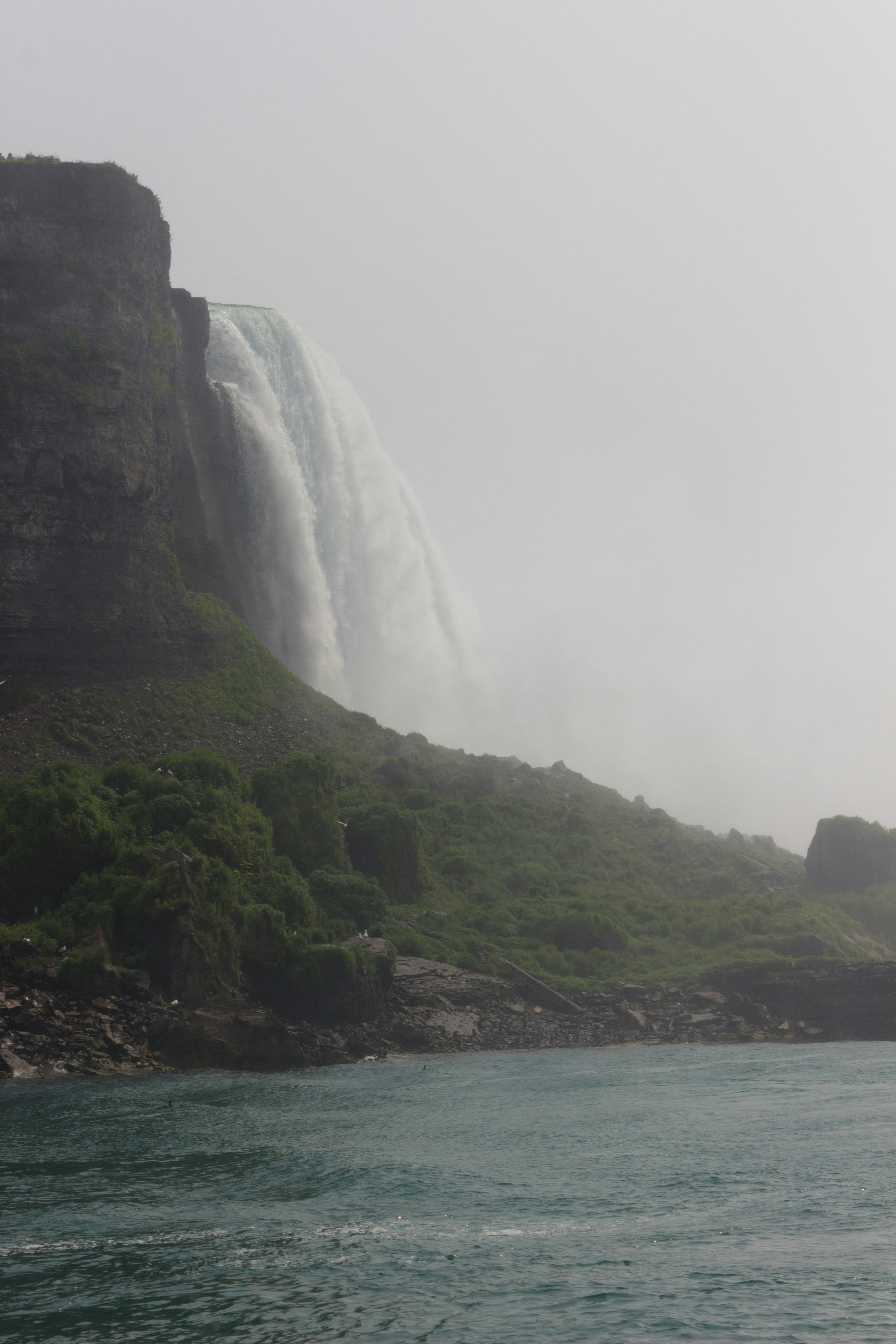Majestic waterfall cascading down rocky cliffs, enveloped in mist, with lush greenery framing the scene. The tranquil water below reflects the surrounding landscape.