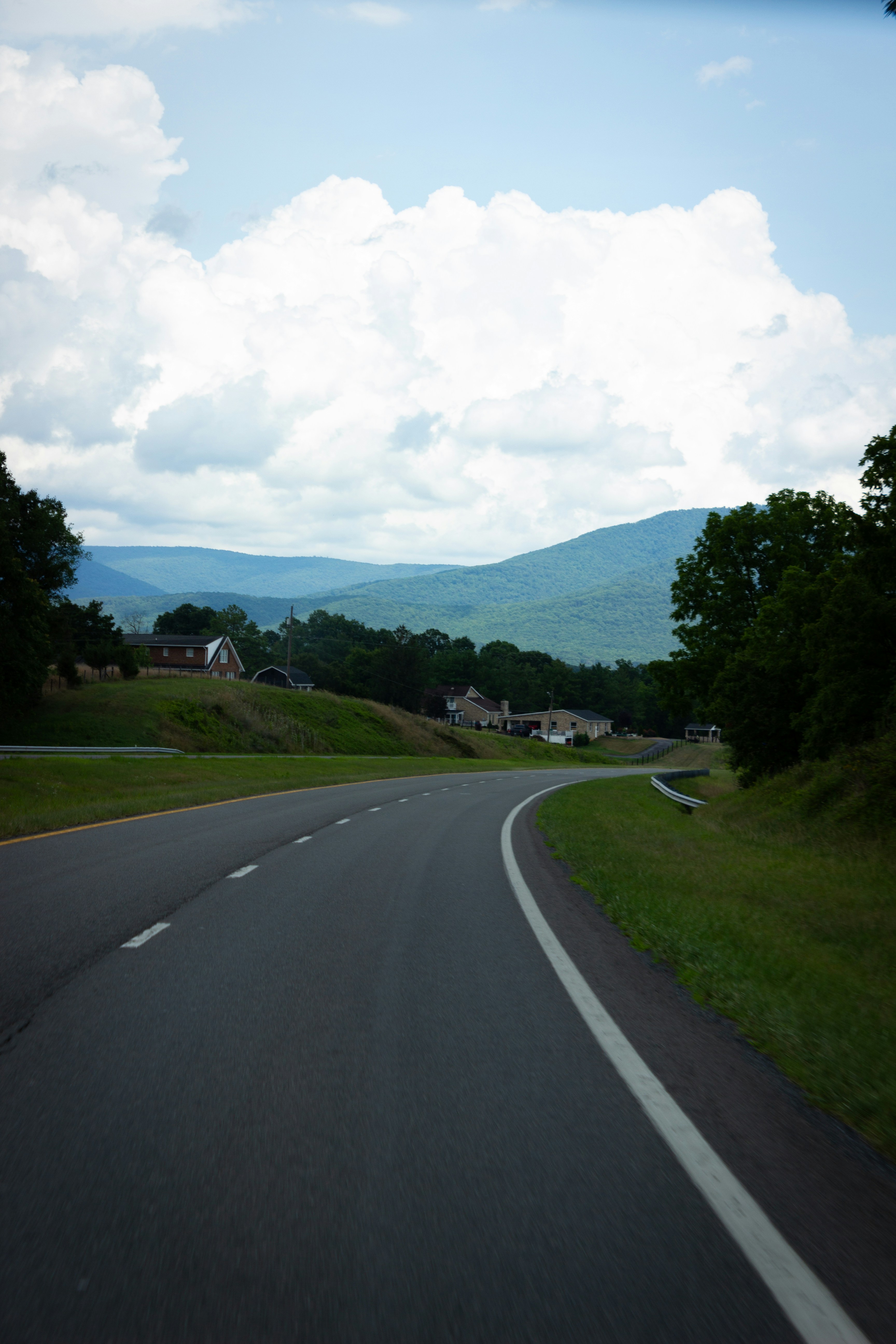 Curving asphalt road through green countryside with mountains.