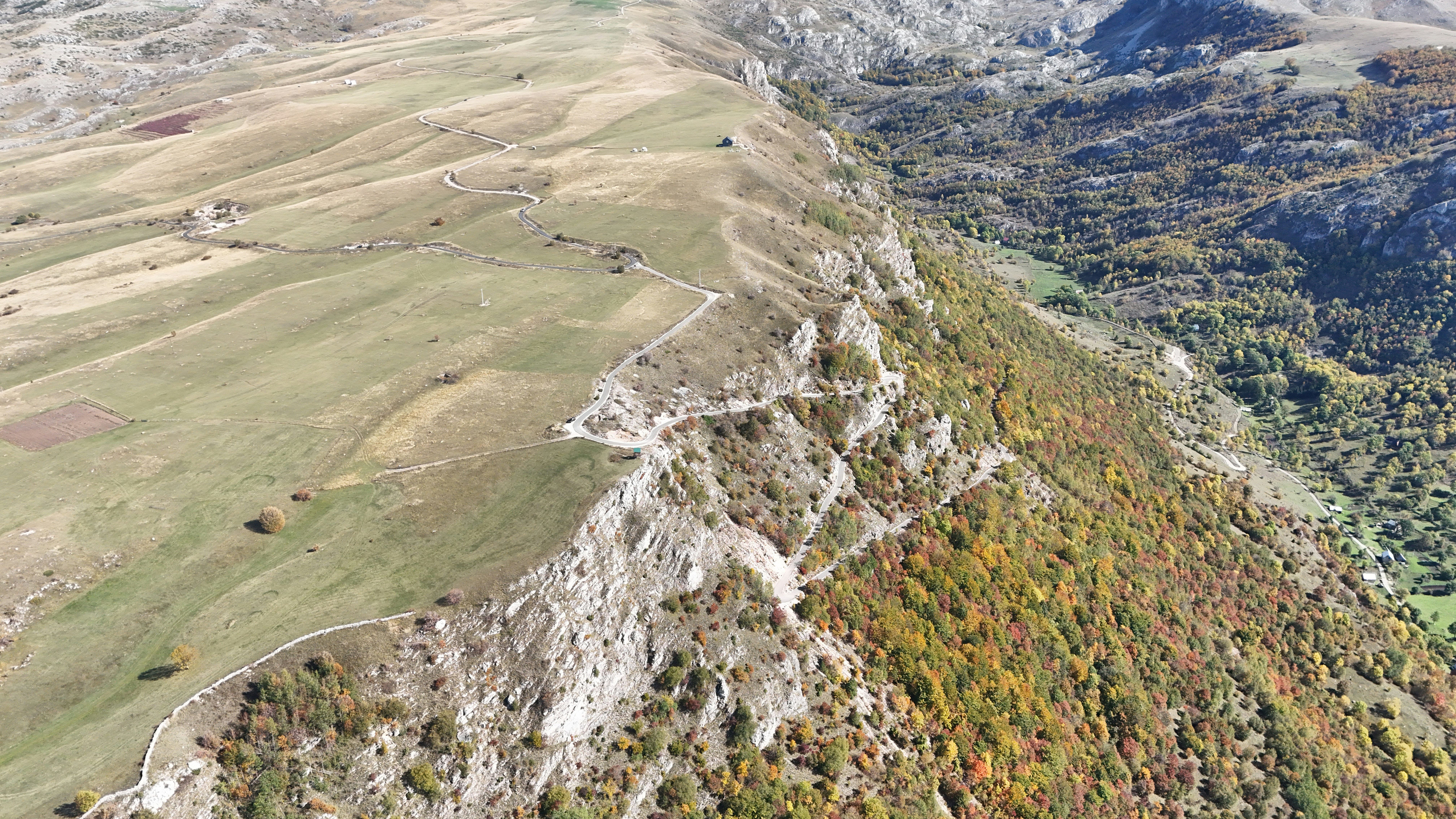 Winding trail cuts through vibrant autumn foliage on a rugged hillside, showcasing the contrast between the rocky terrain and colorful trees. 