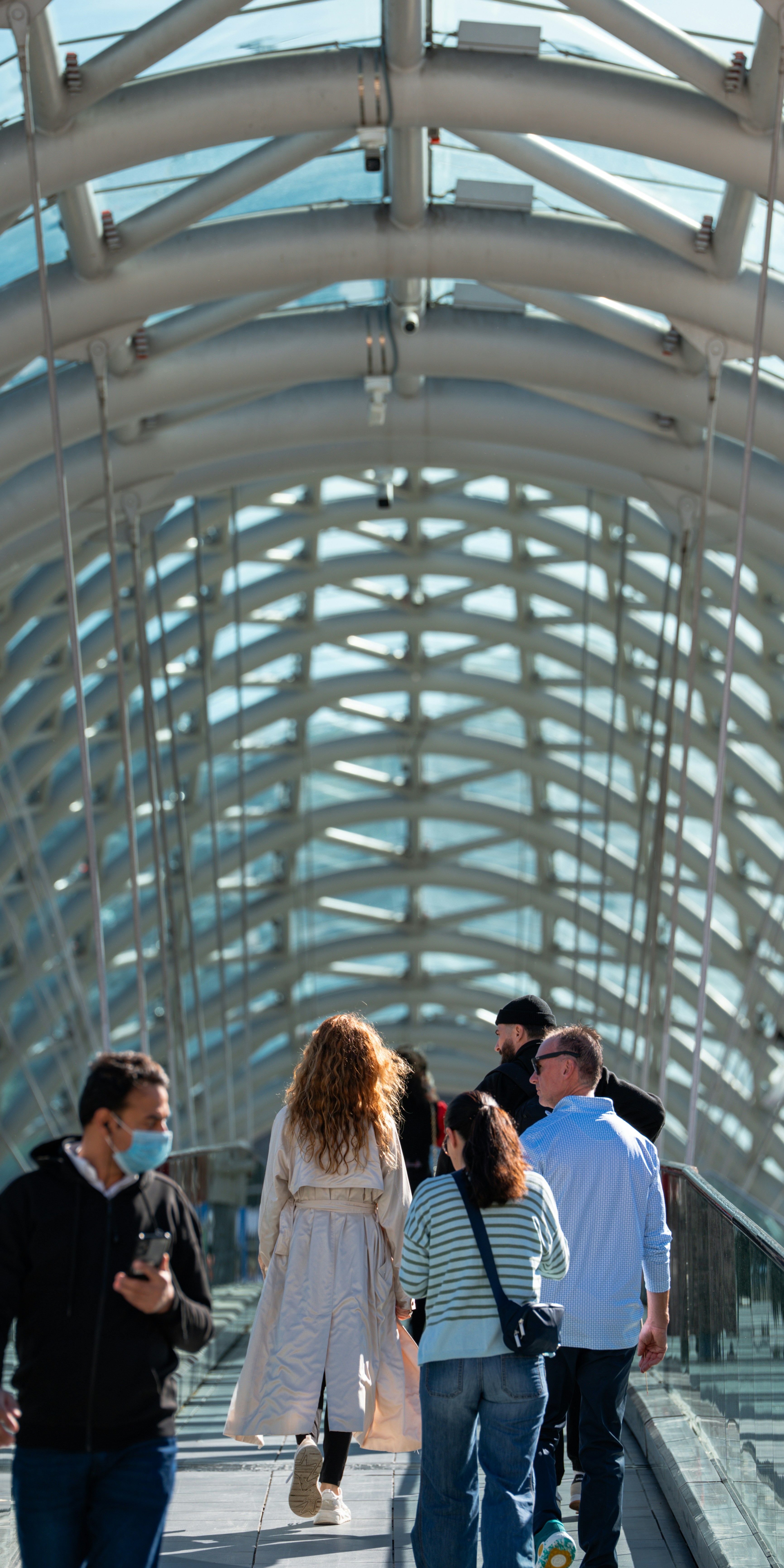 People walking through a modern glass and metal walkway.