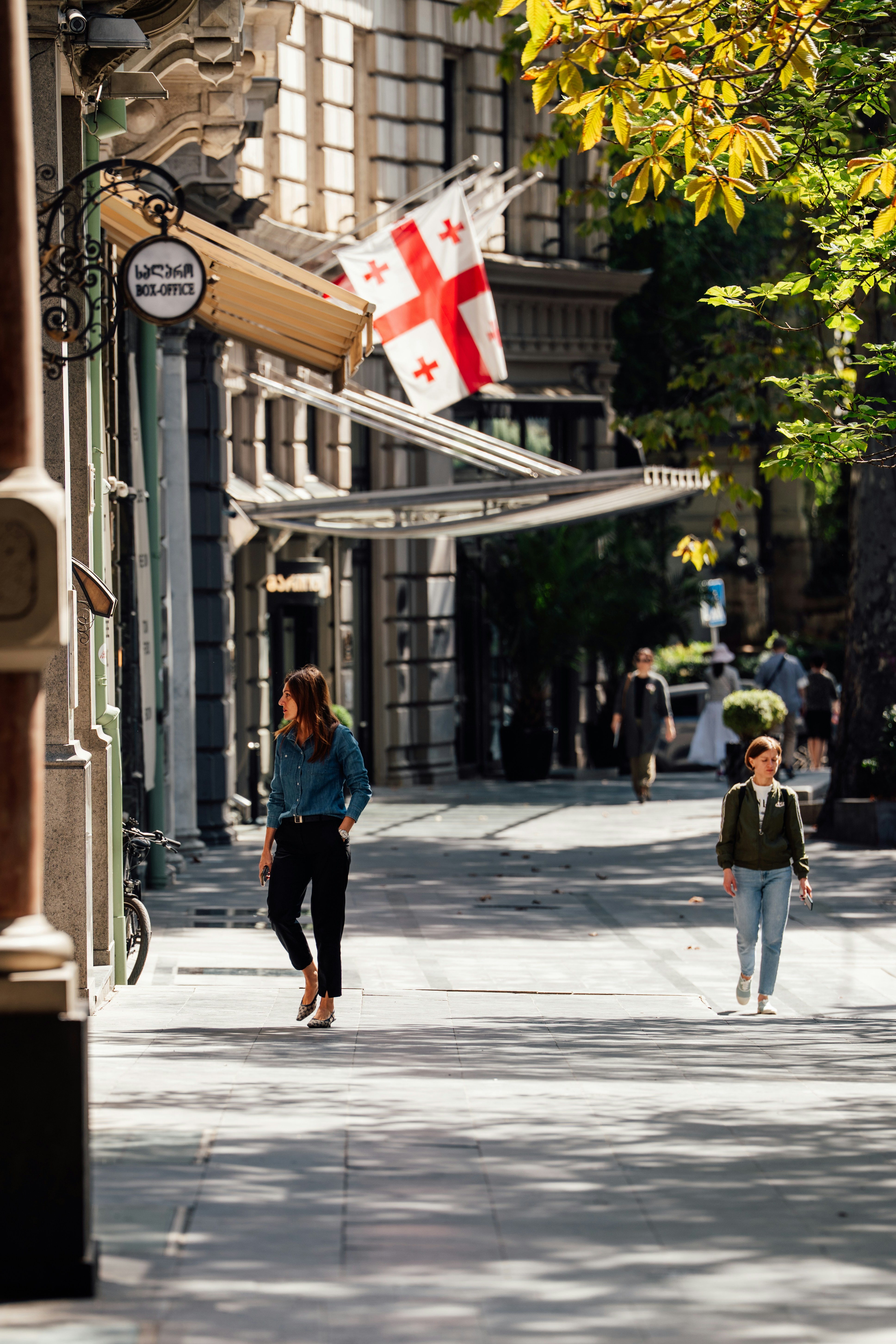 People walking on a sunny street with georgian flag.