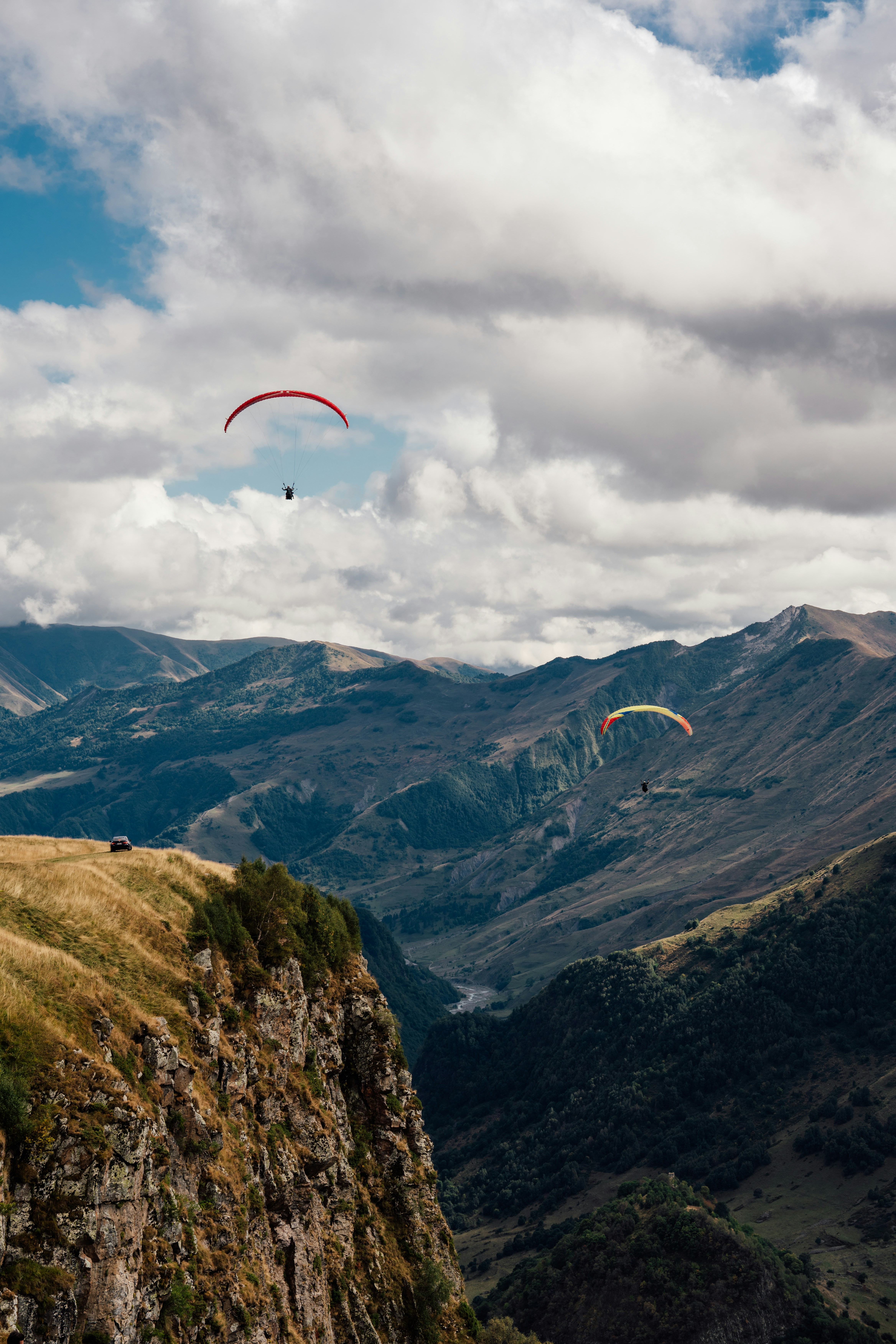 Paragliders soar over a dramatic mountain landscape.
