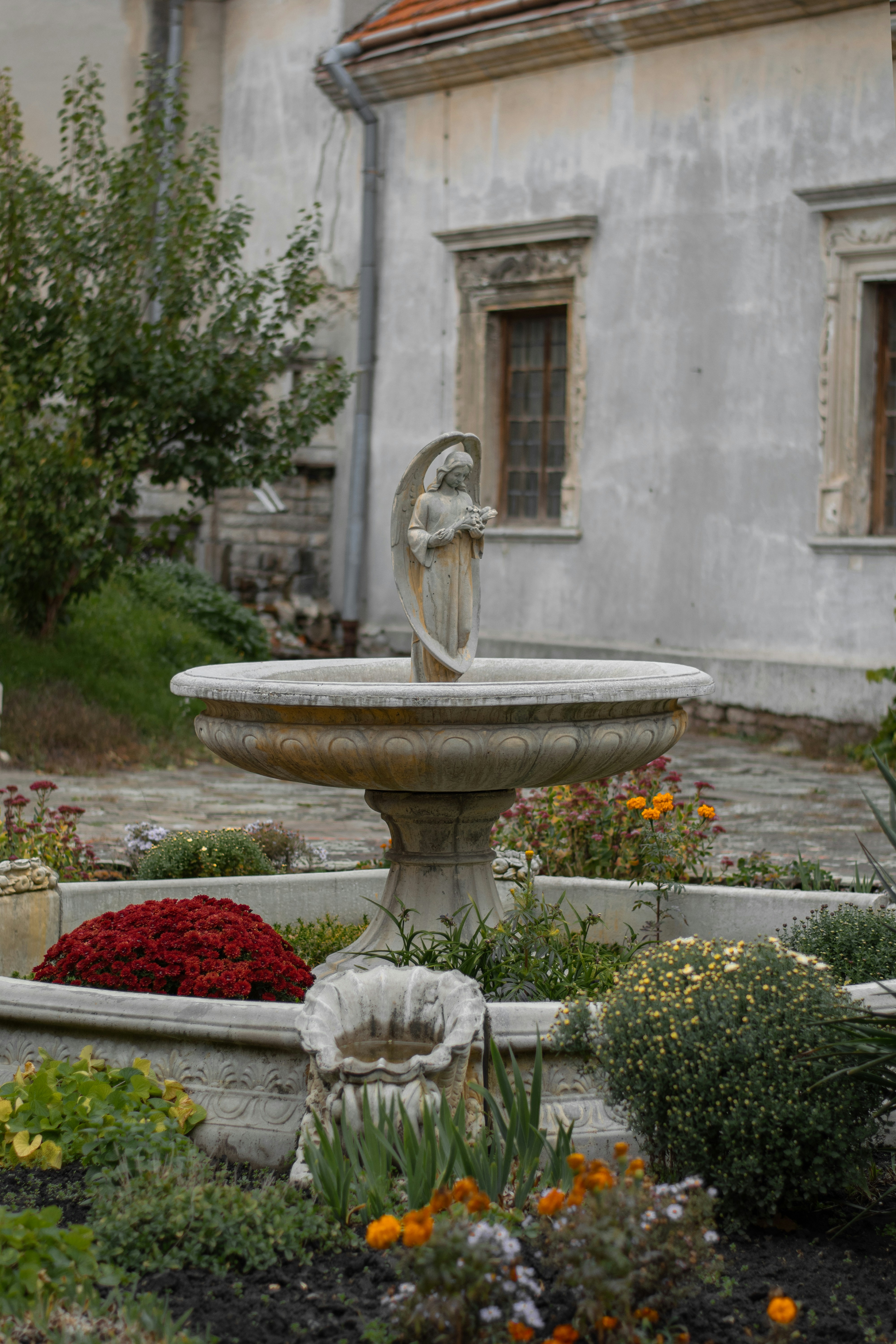 Stone angel fountain surrounded by colorful flowers
