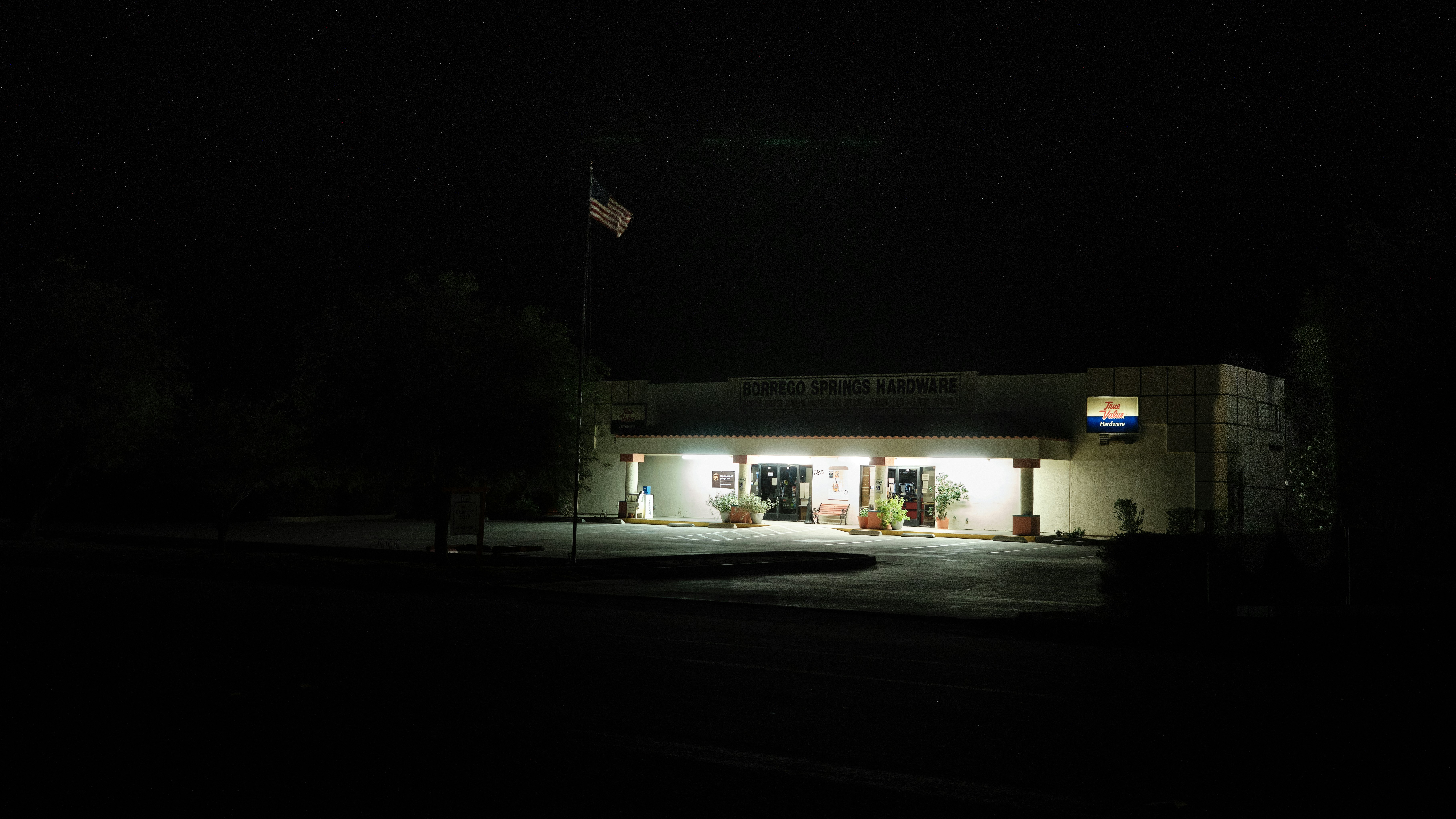 “The last light in town” | Building illuminated at night with a flag pole.
