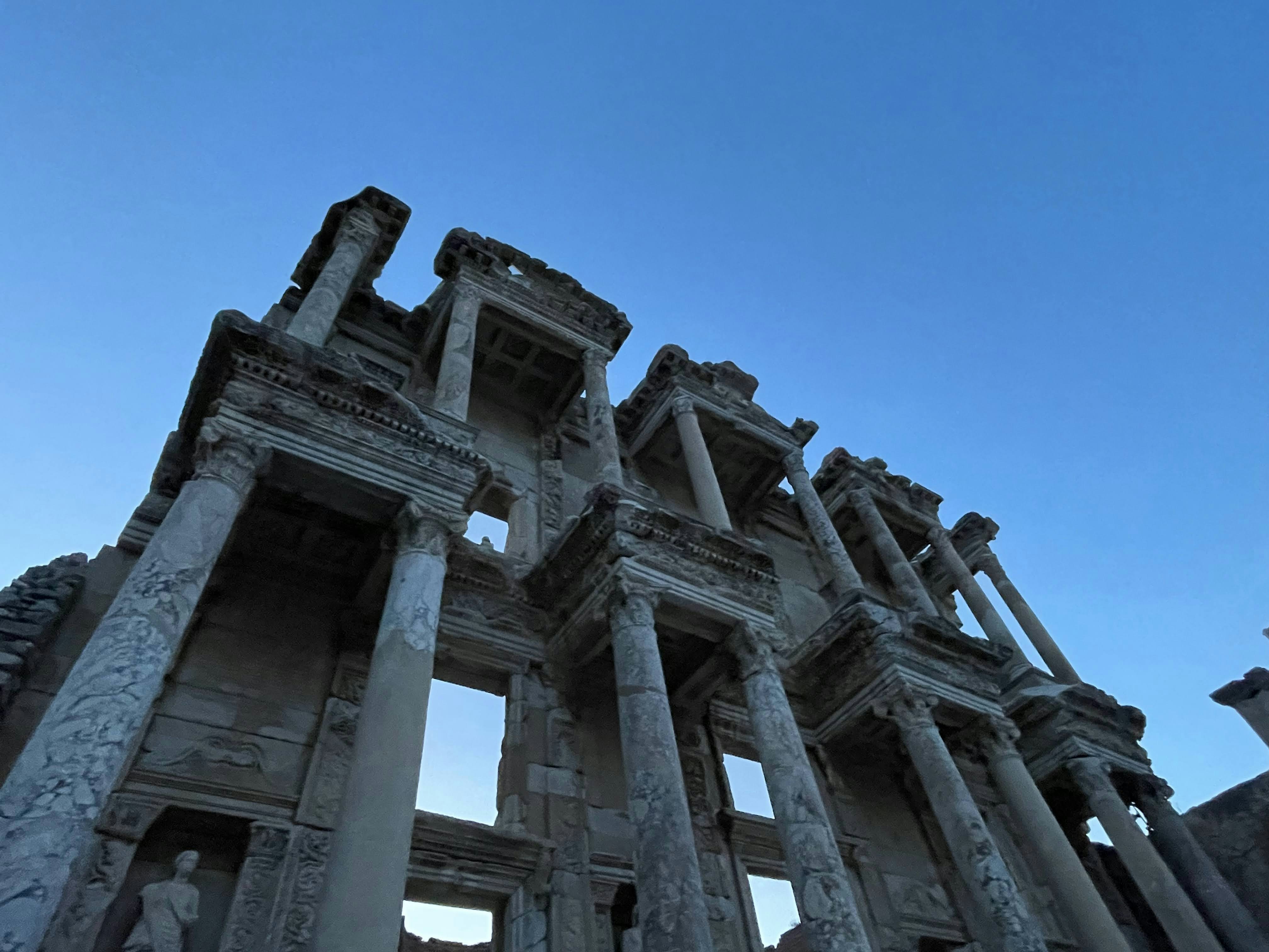 The grand facade of a historic ruin stands against a clear blue sky, showcasing intricate architectural details and weathered stonework.