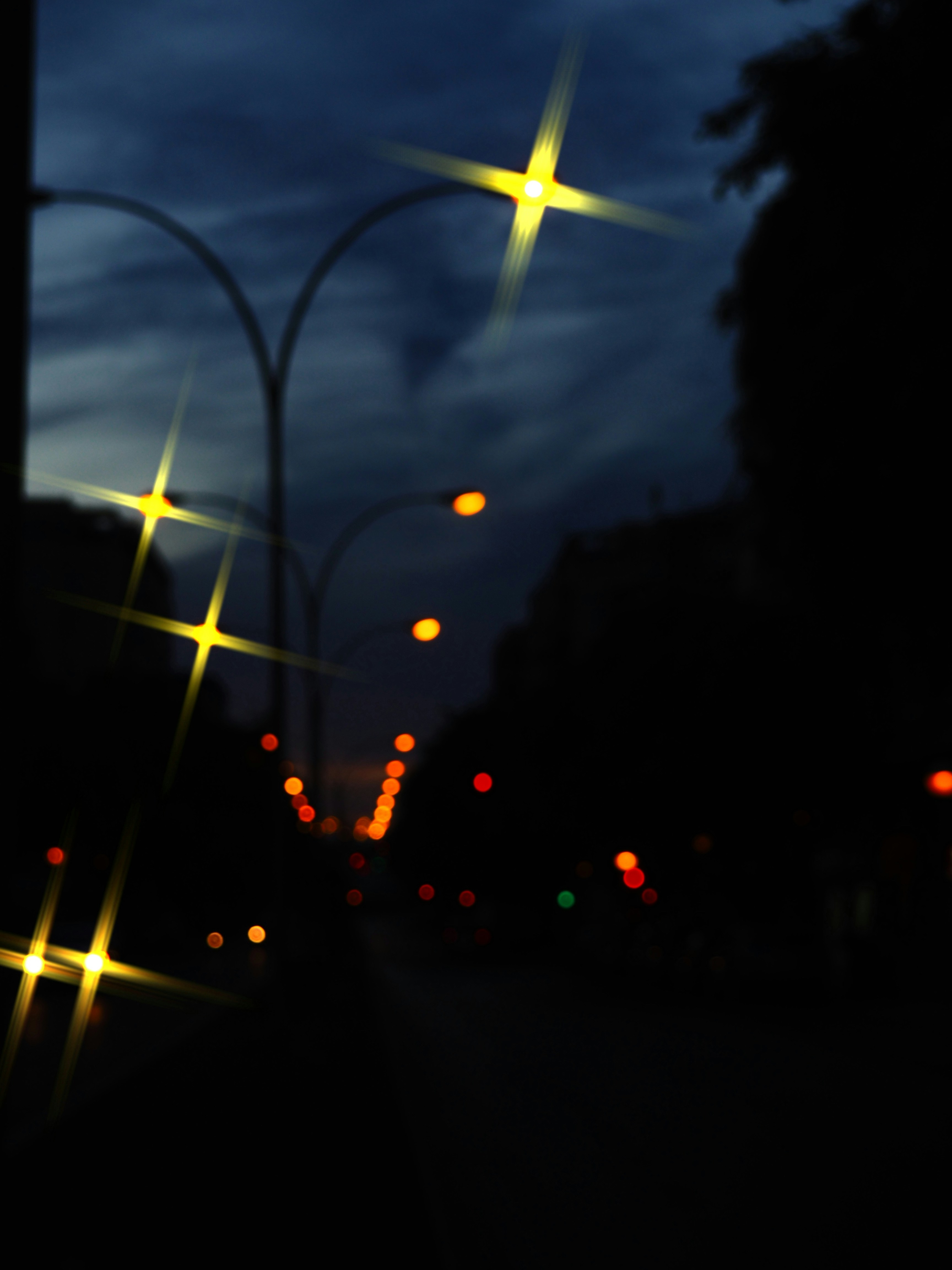 Glowing streetlights illuminate a blurred urban landscape at dusk, creating a dreamy atmosphere with star-like reflections. 