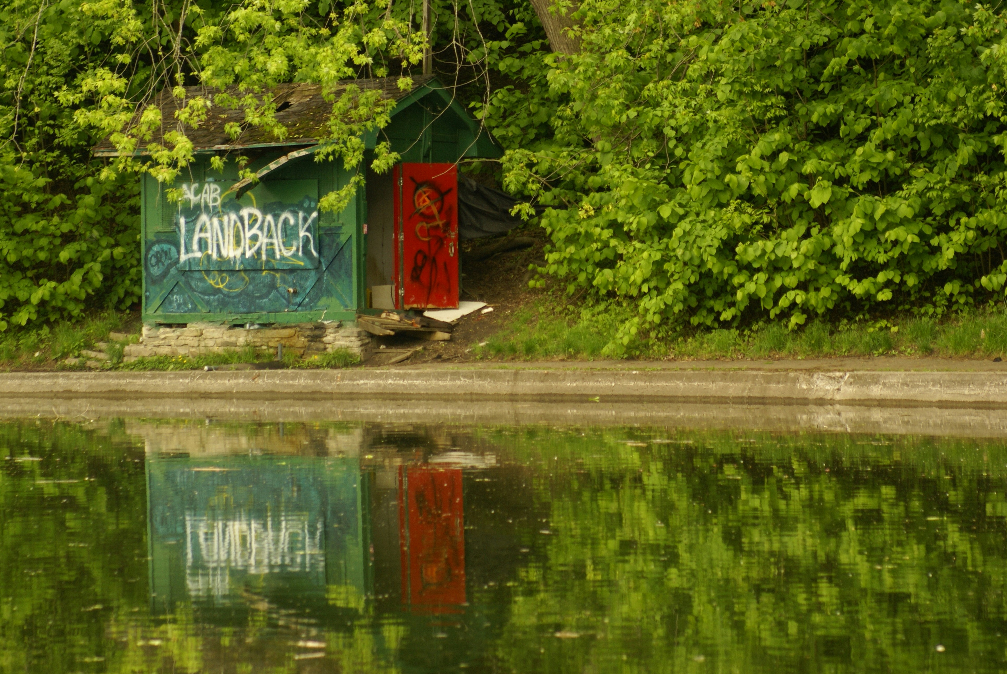 Small shack with graffiti reflected in water.