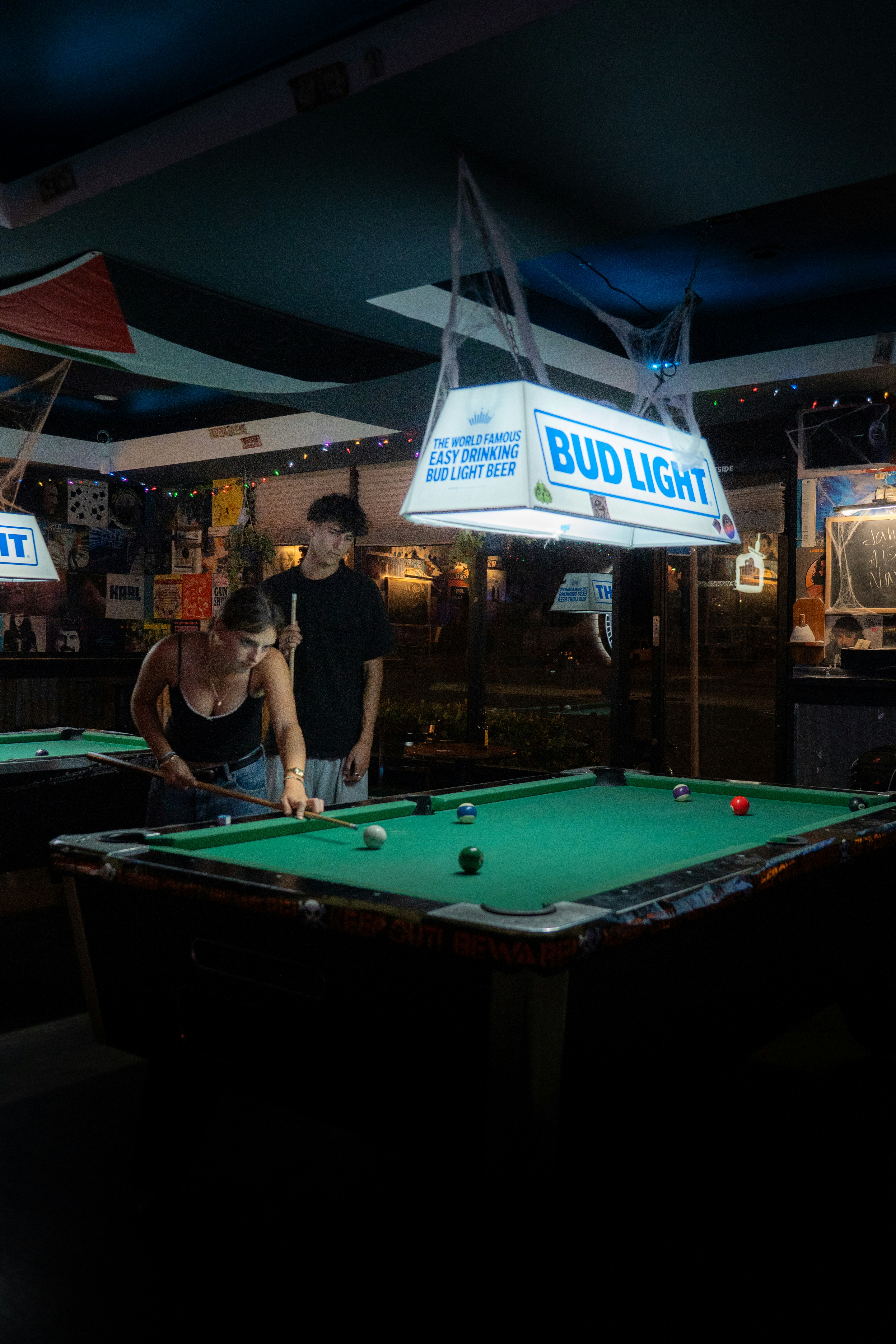 Two people playing pool under a bud light sign.