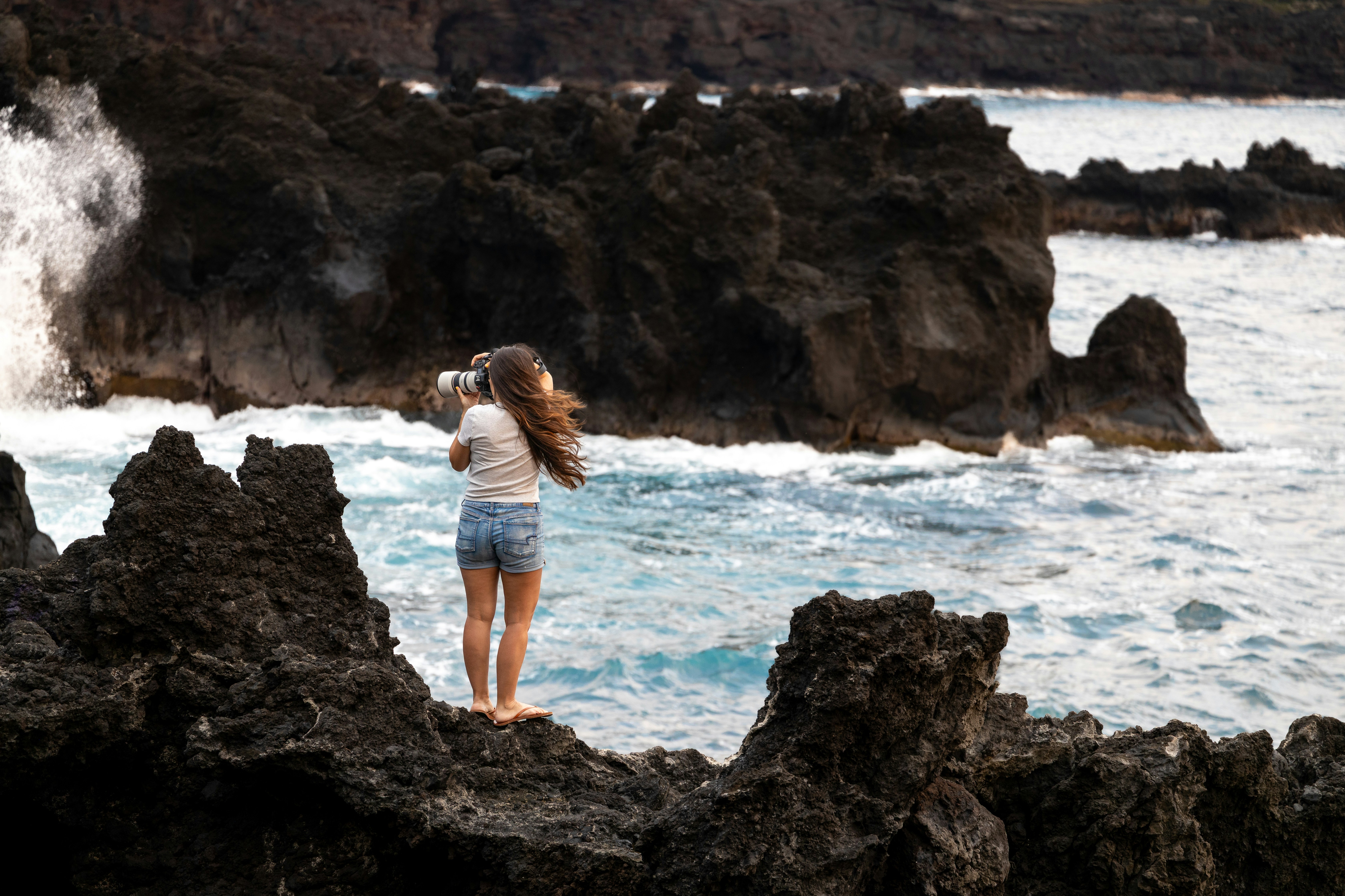 Woman with camera photographing ocean waves on rocky shore