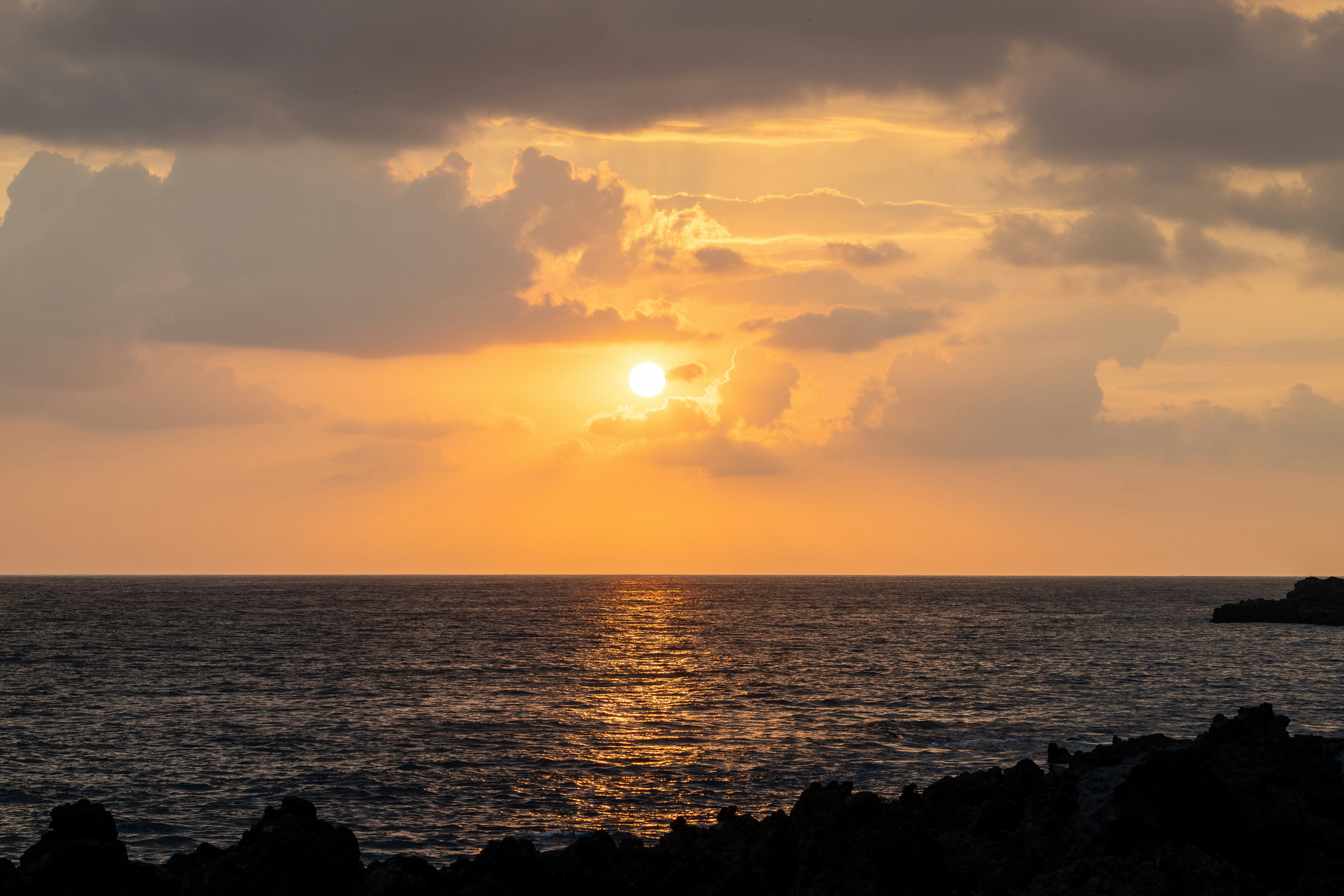 Sunset over a calm ocean with dark foreground