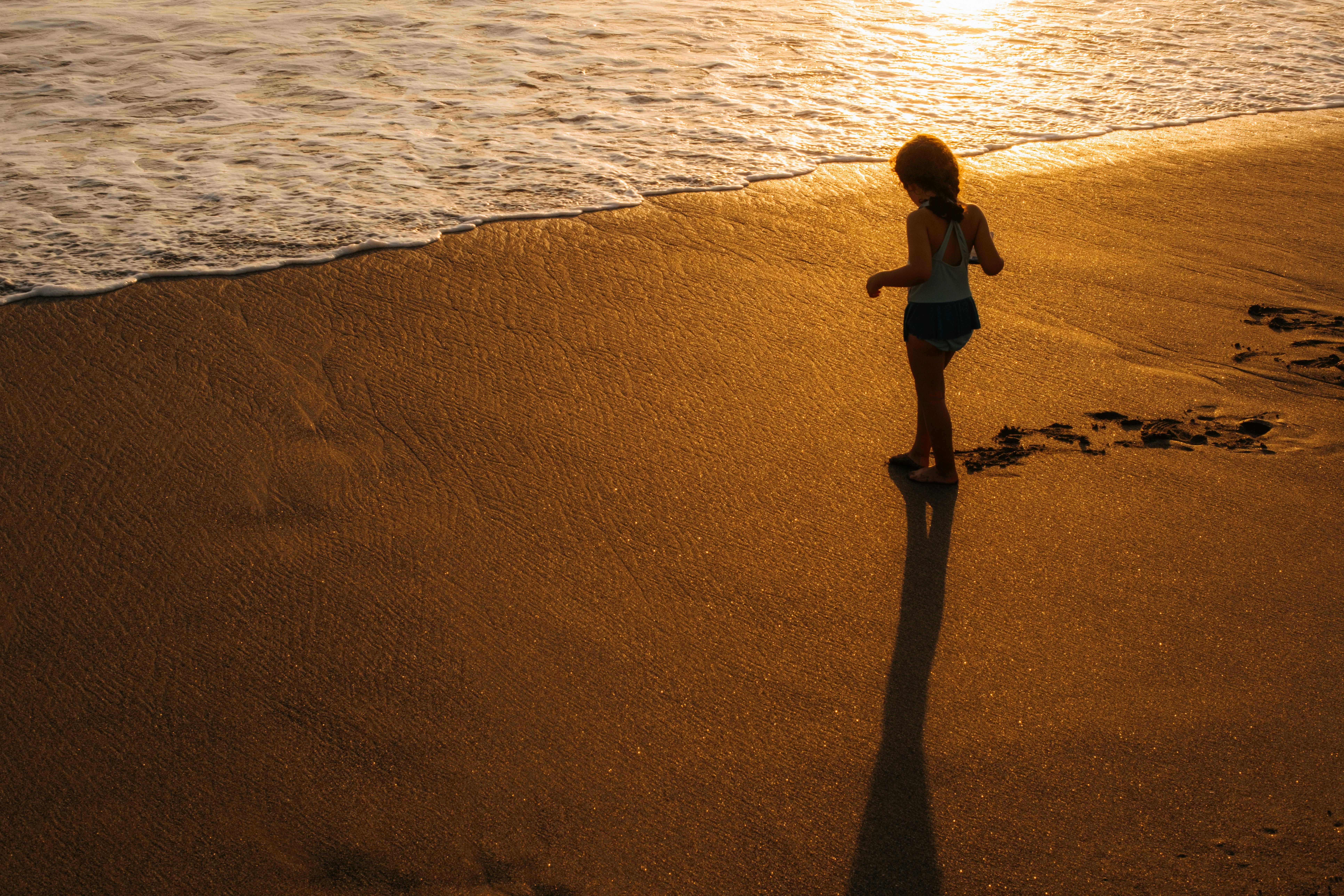 A child plays on a sandy beach at sunset.