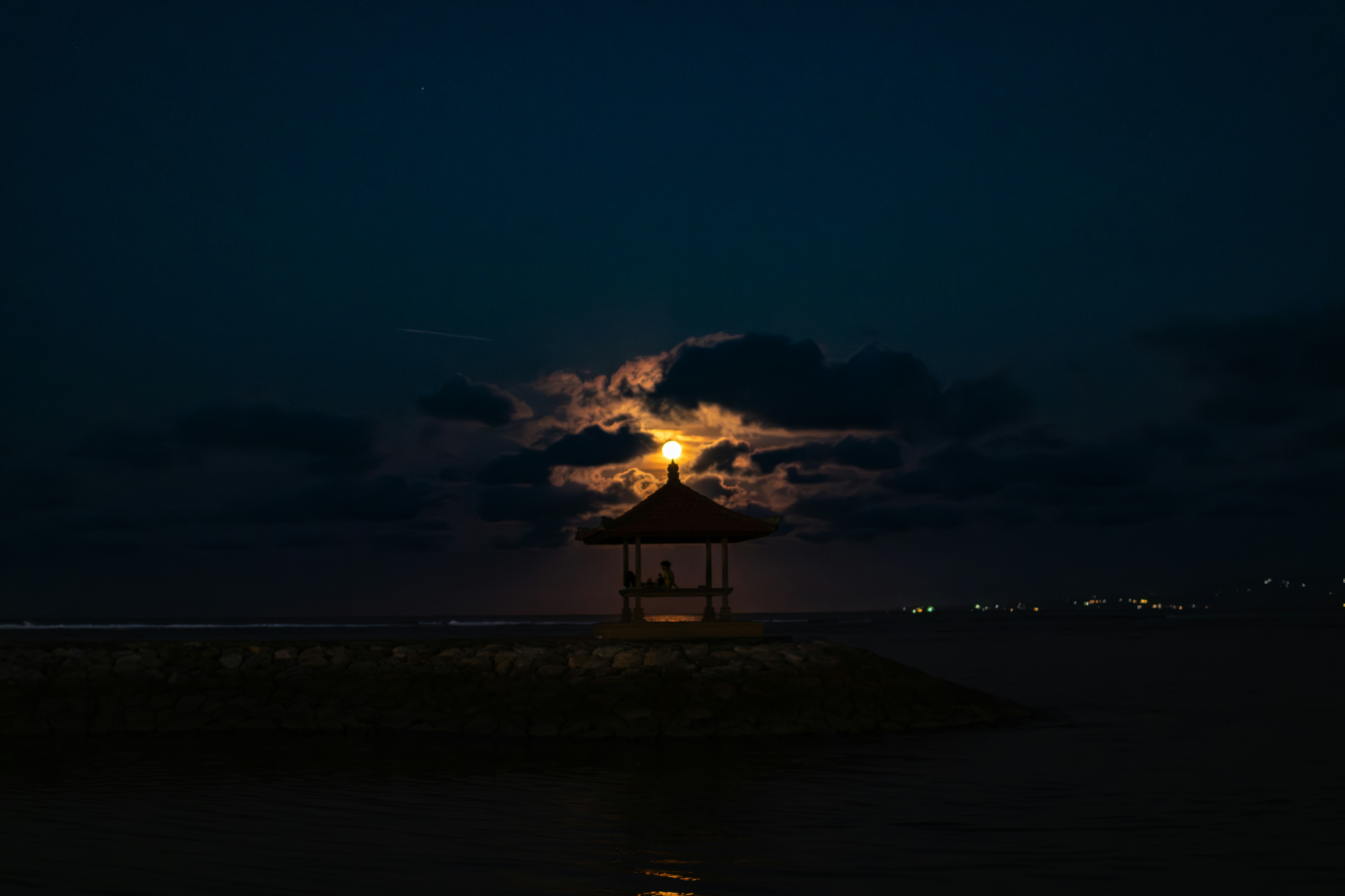 Full moon behind clouds over a small hut.