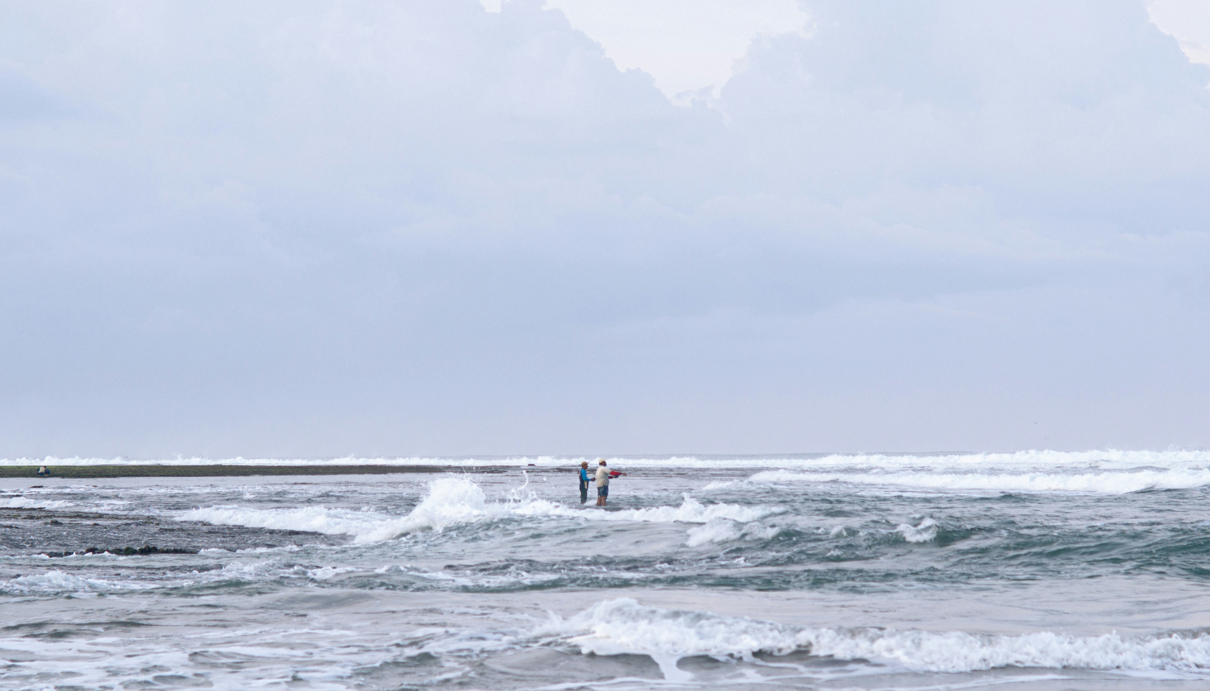 Two figures navigating the turbulent ocean waves under a cloudy sky.