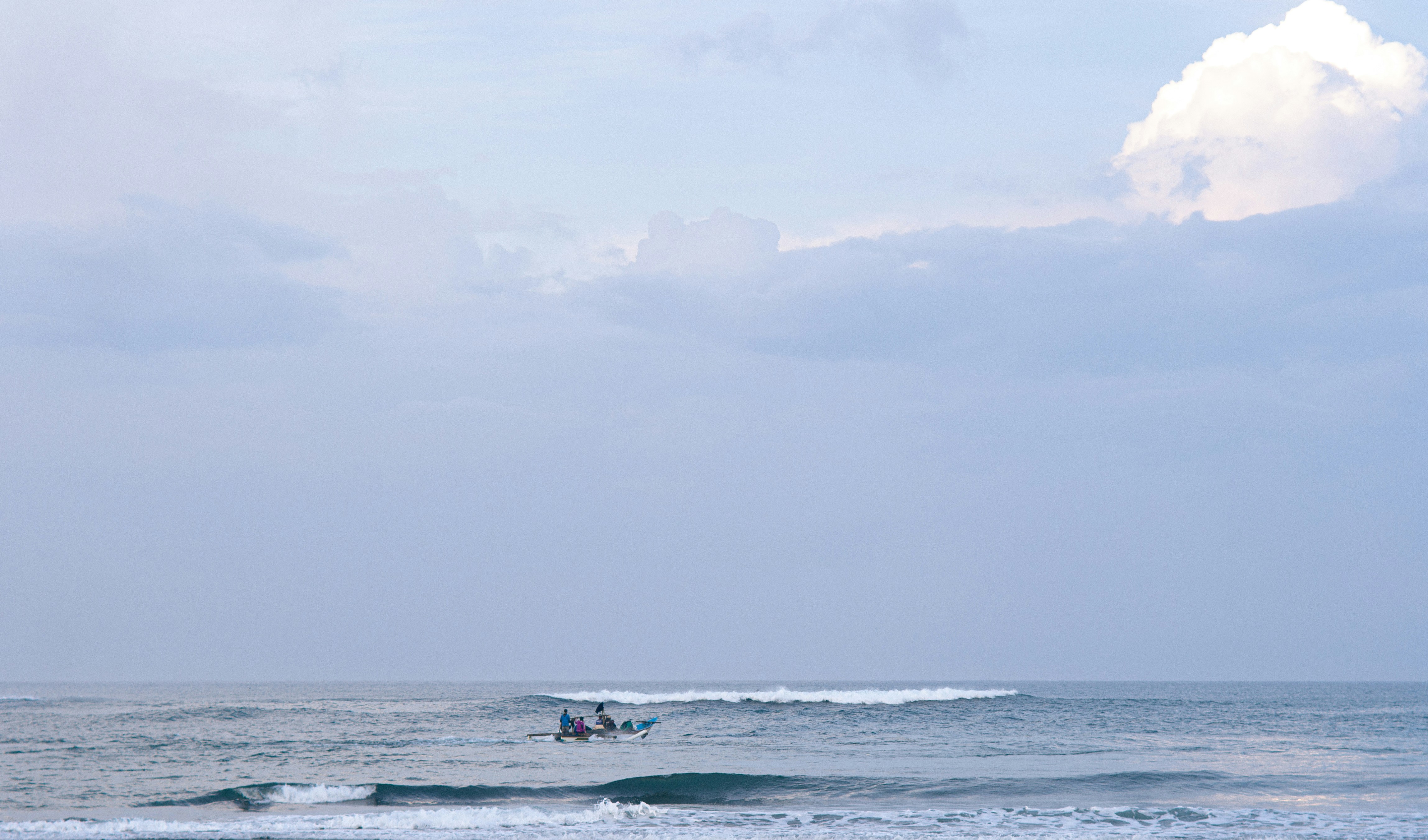 OLYMPUS DIGITAL CAMERA | Surfers ride waves under a cloudy sky.