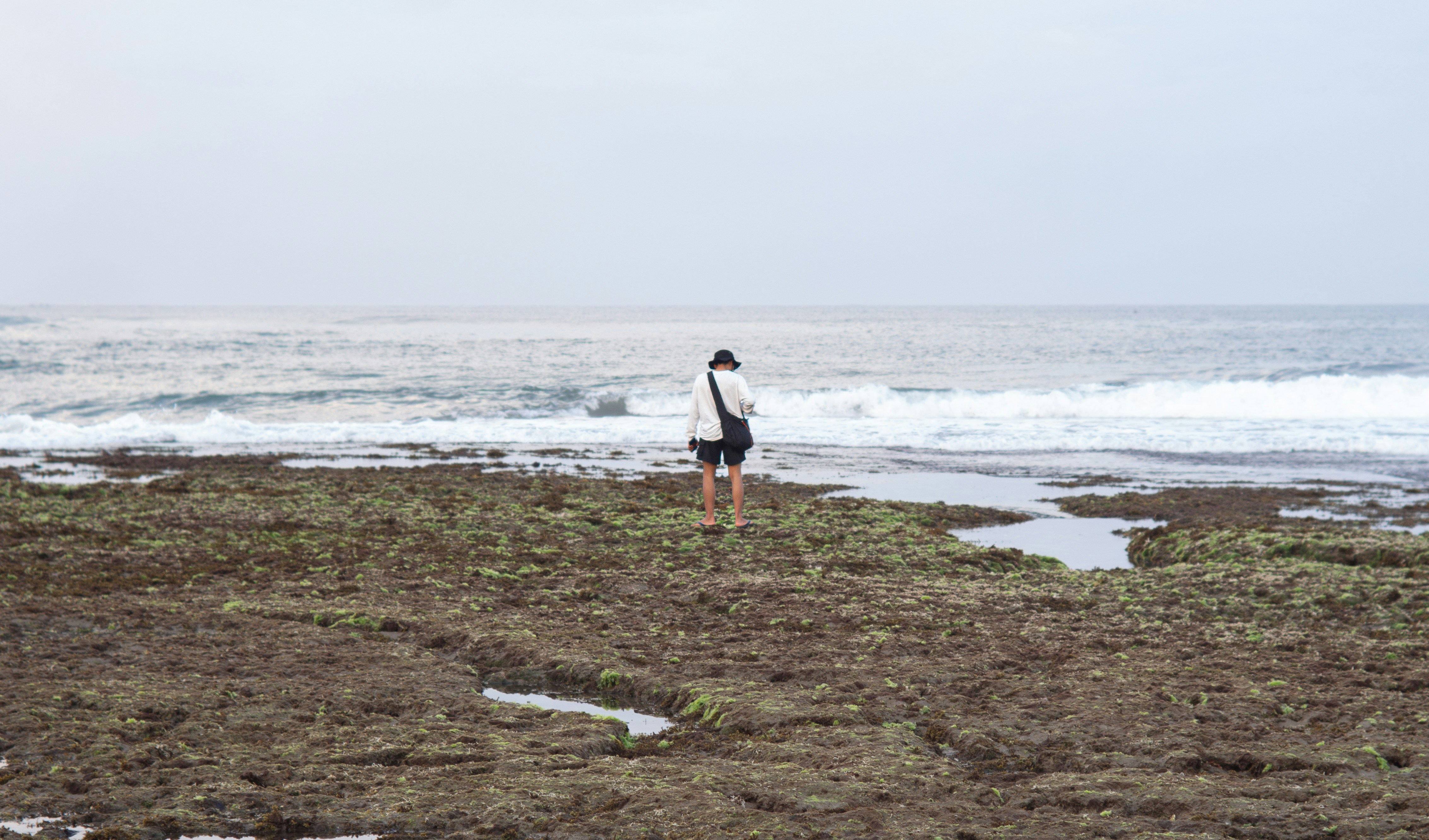 OLYMPUS DIGITAL CAMERA | Person standing on a rocky shore by the ocean.