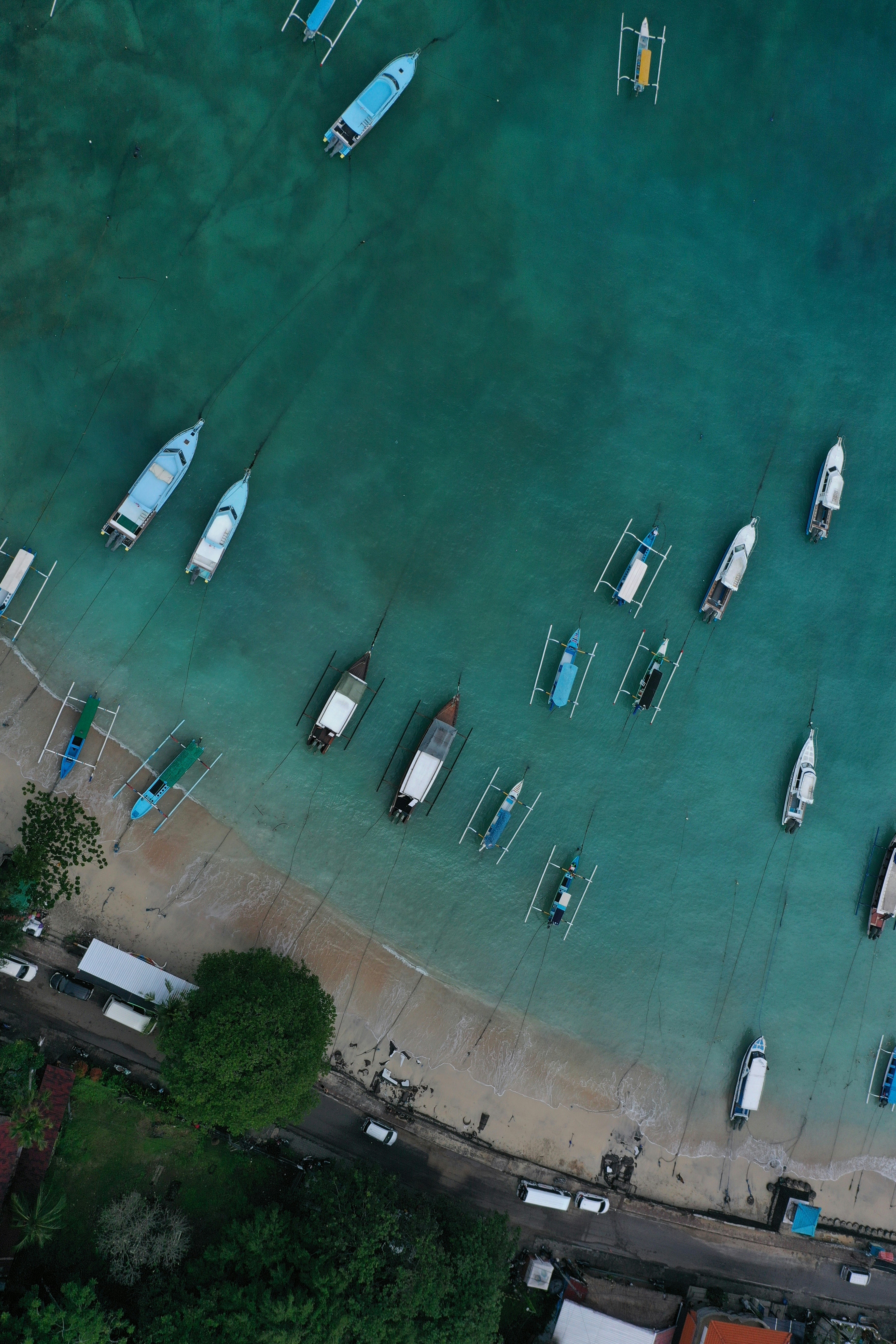 Many boats docked in clear turquoise water near shore.