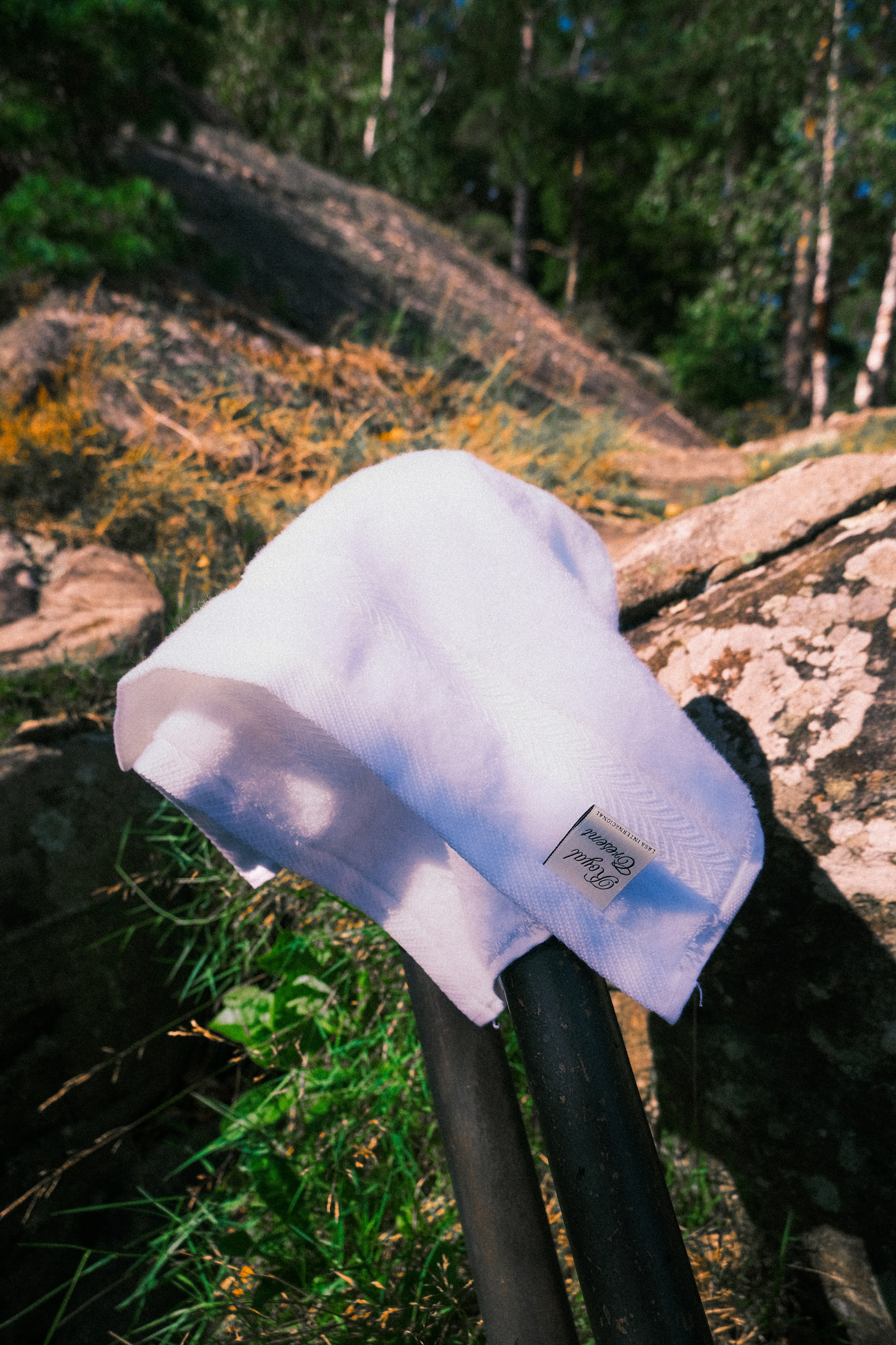 A white cotton towel resting on sun-warmed rock. | White towel resting on a dark pole outdoors.