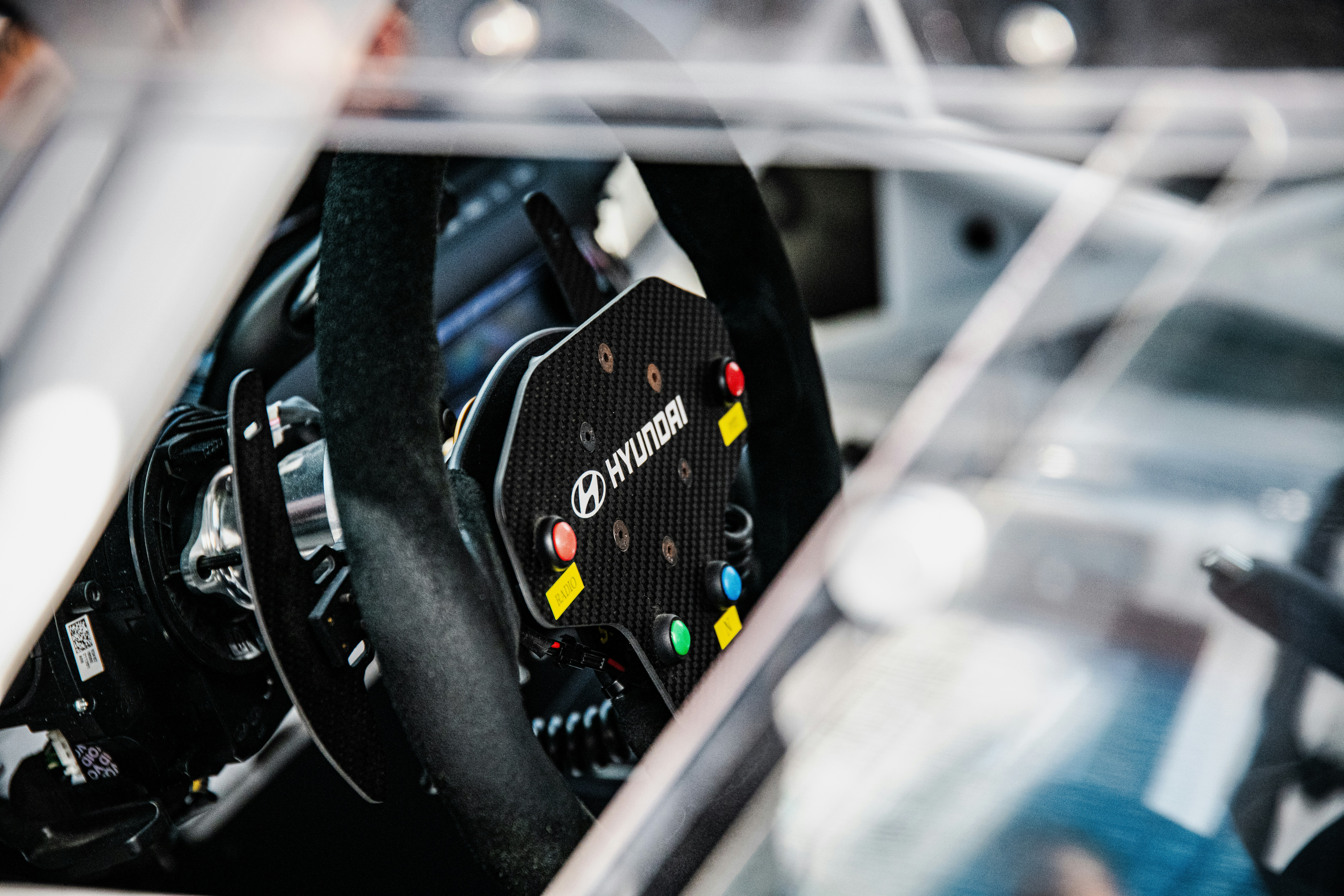 Close-up of a high-tech racing steering wheel featuring buttons and a carbon fiber design, showcasing advanced engineering in motorsport.