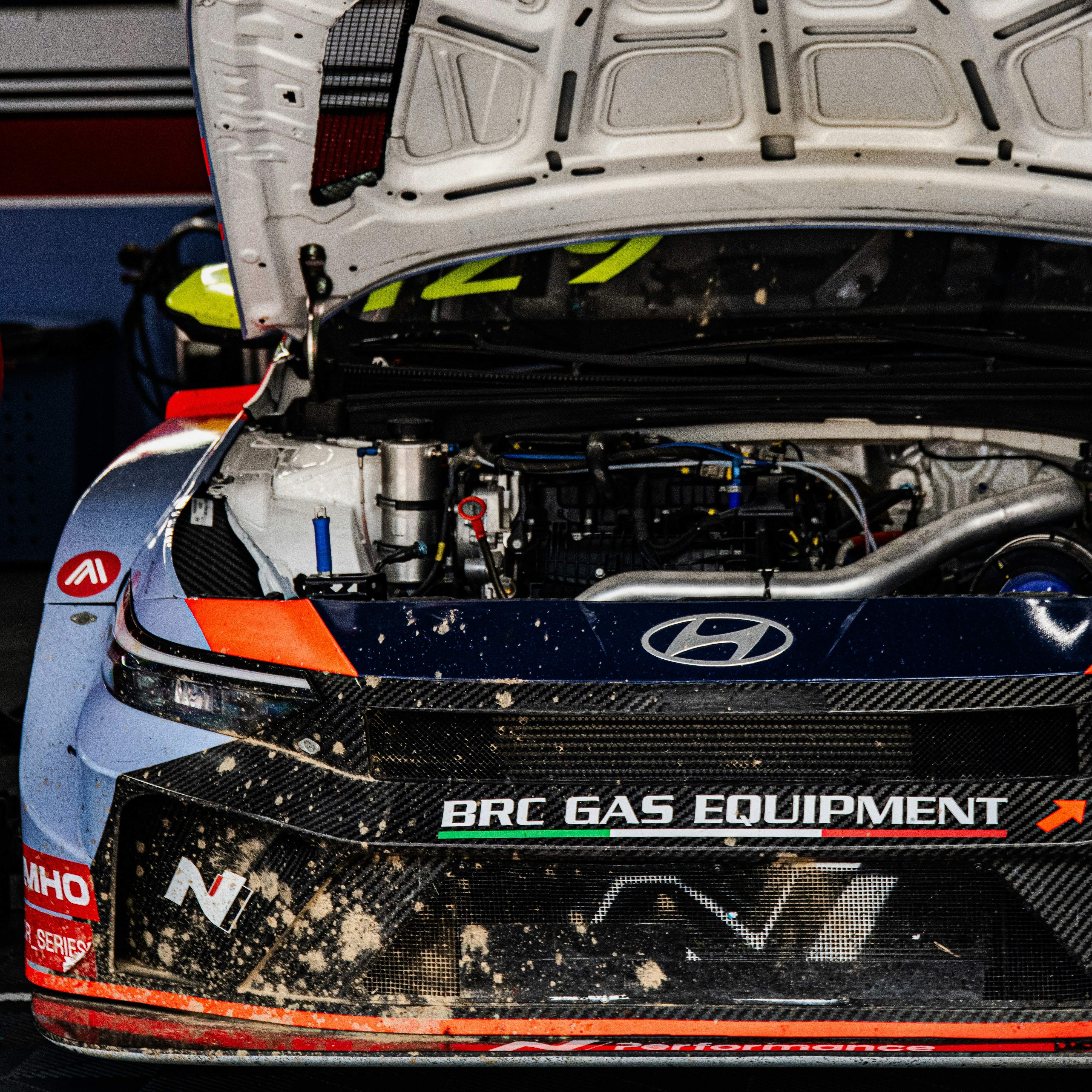 Race car with hood open showing engine and mud splashes.