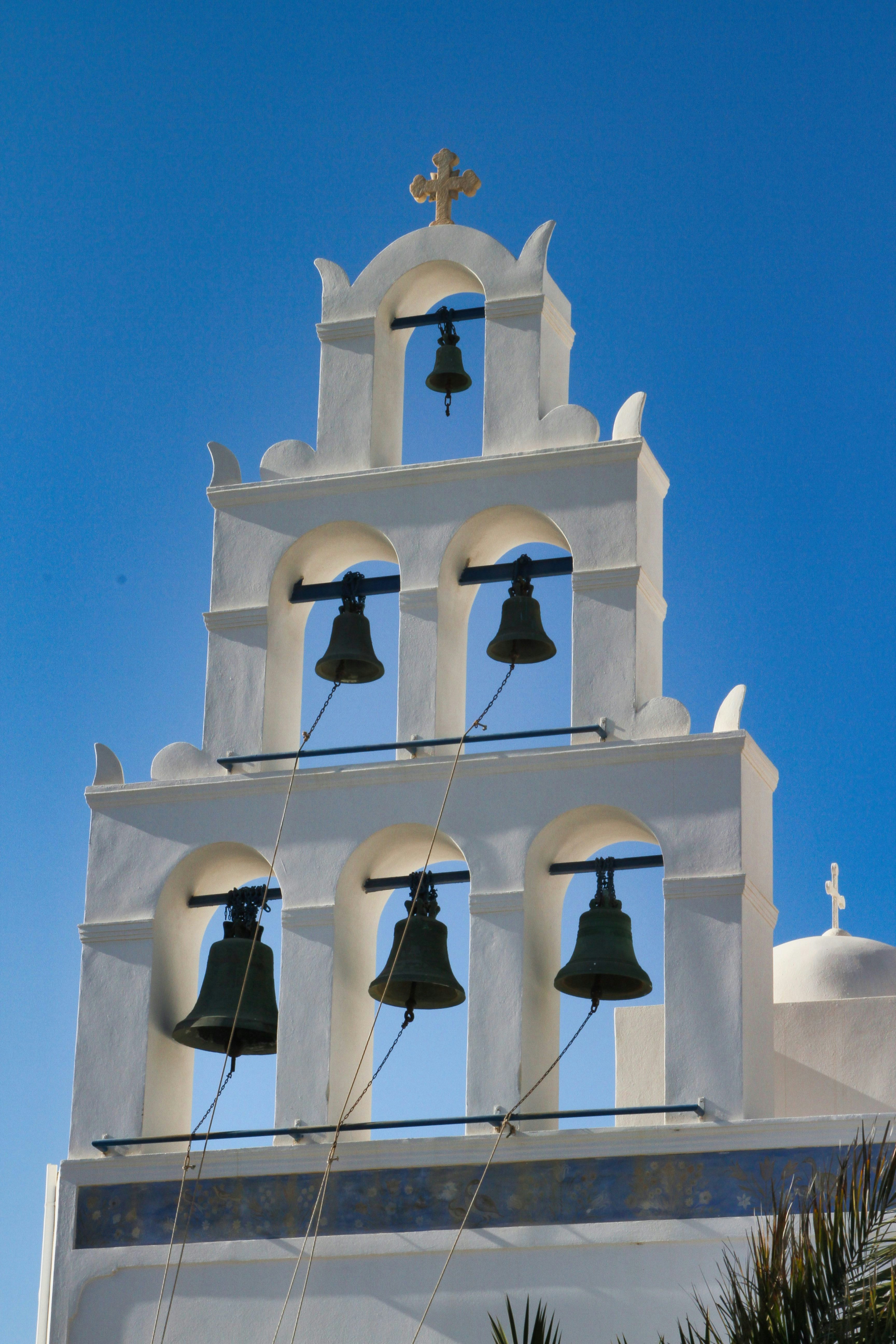 White bell tower with multiple bronze bells against blue sky